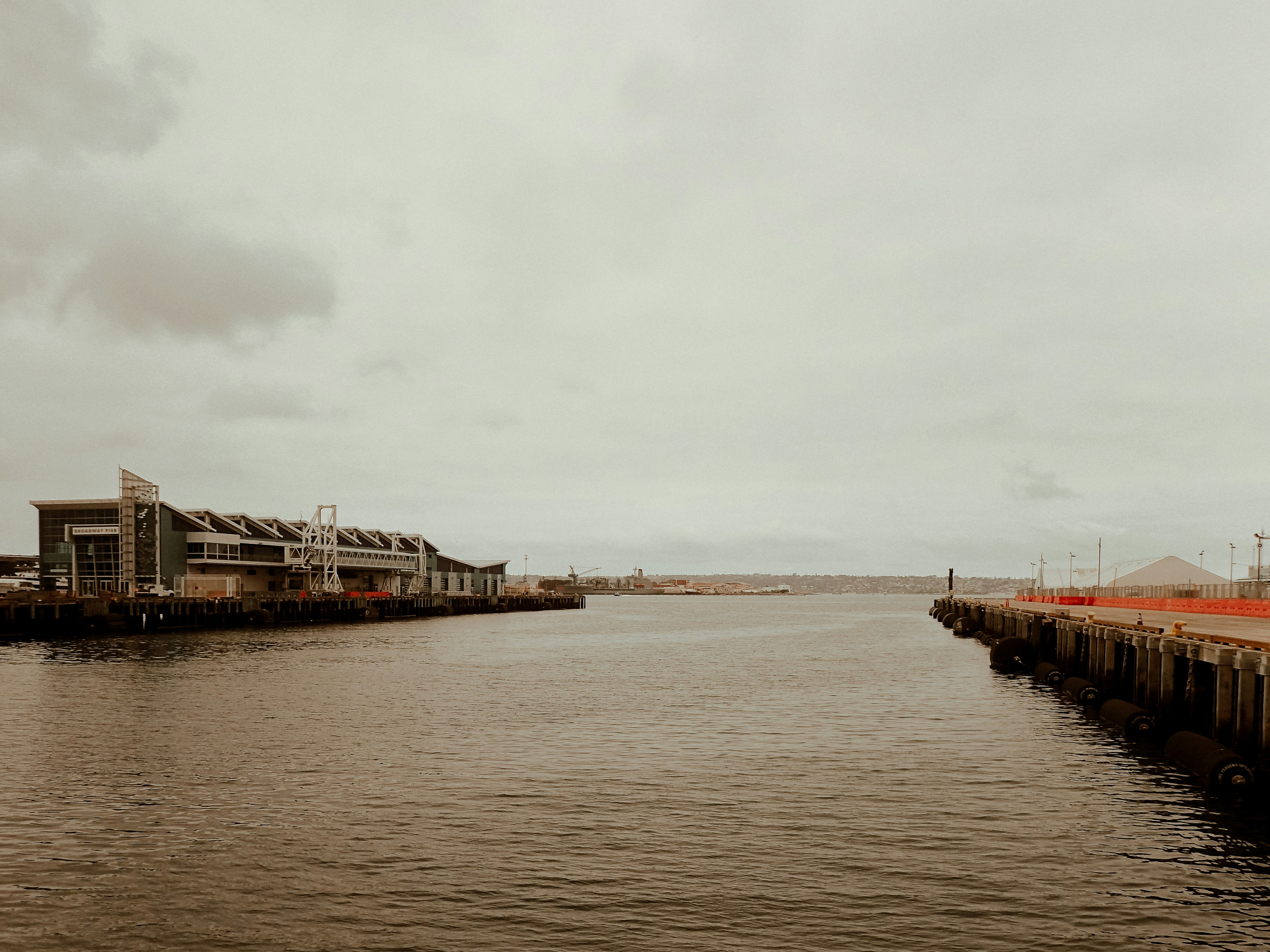Industrial waterfront scene with calm waters reflecting the overcast sky and nearby structures along the pier.