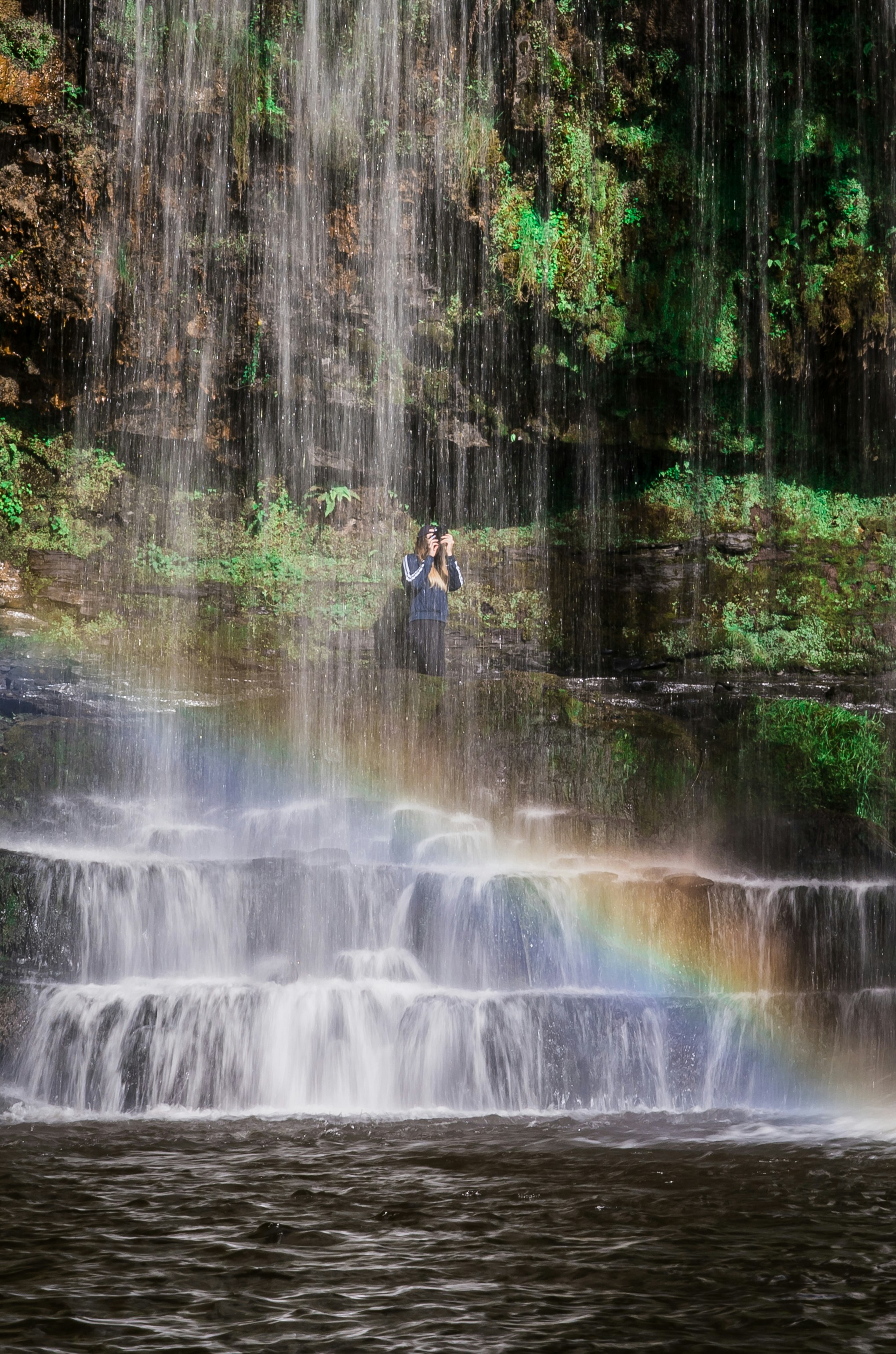 Person in black jacket and black pants standing on rock near waterfalls ...
