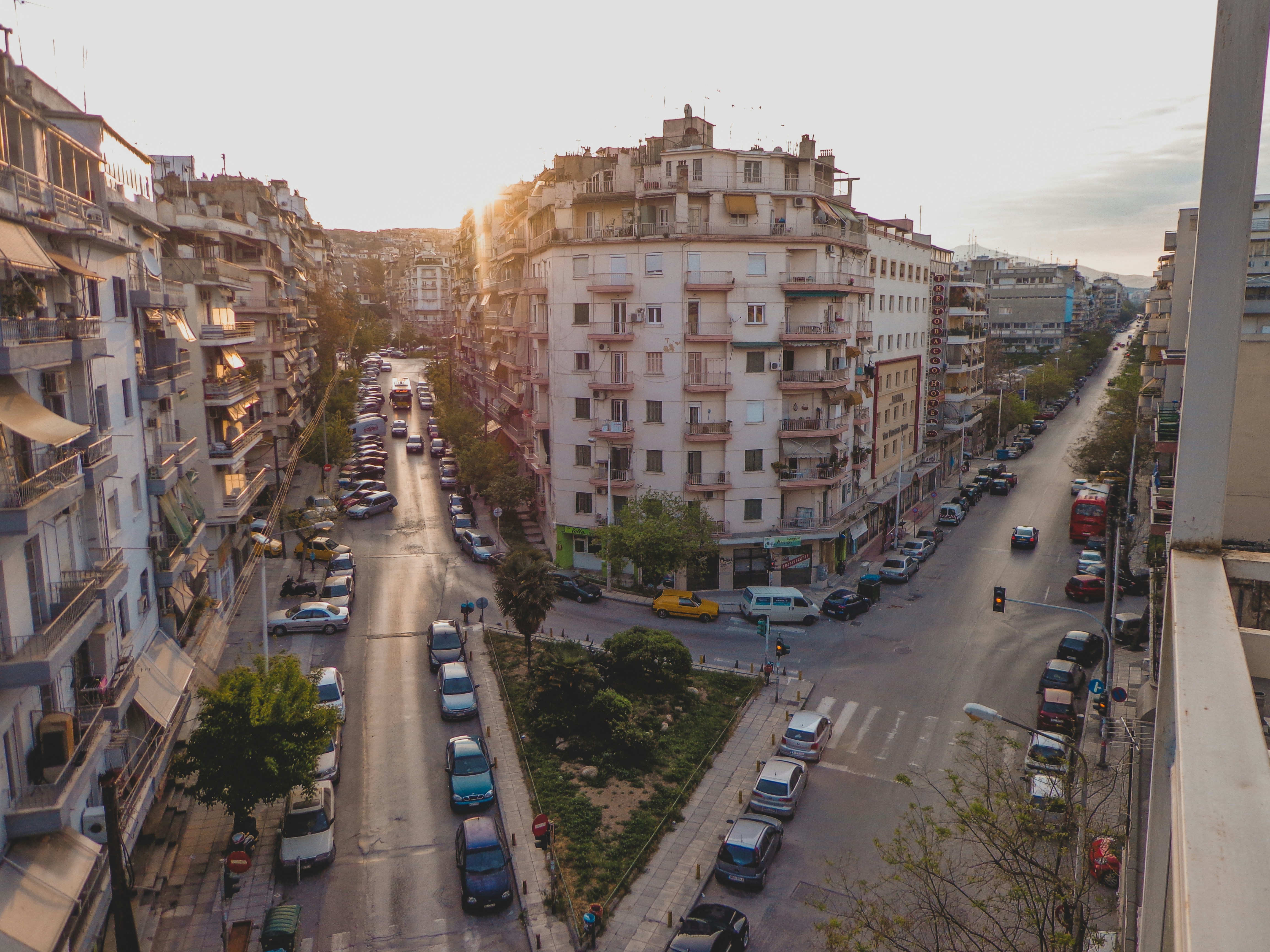 Sunset light casts a warm glow on a bustling Athens street lined with parked cars and residential buildings.