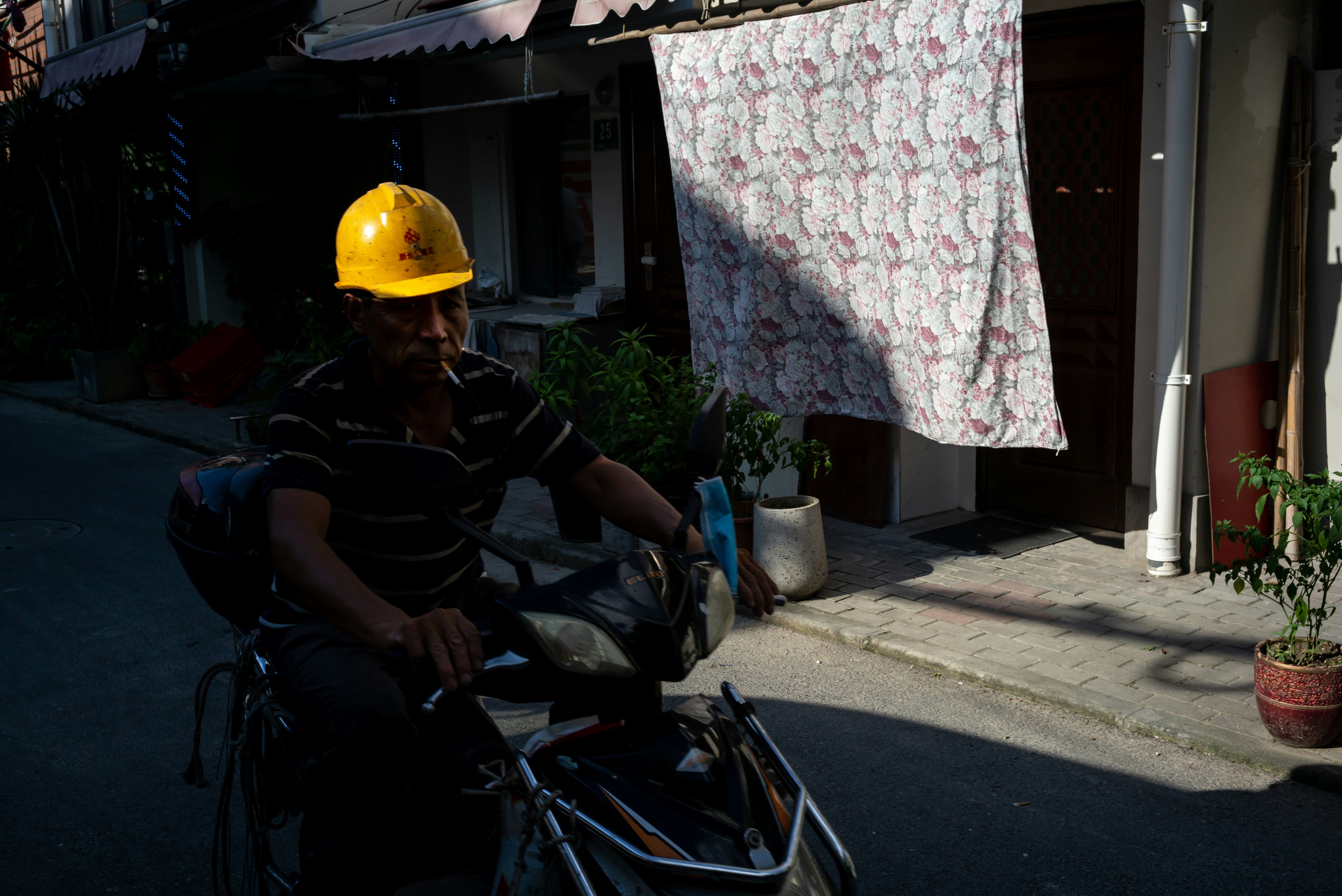 Yellow-helmeted Rider in a Narrow Street Framed by a Floral Curtain