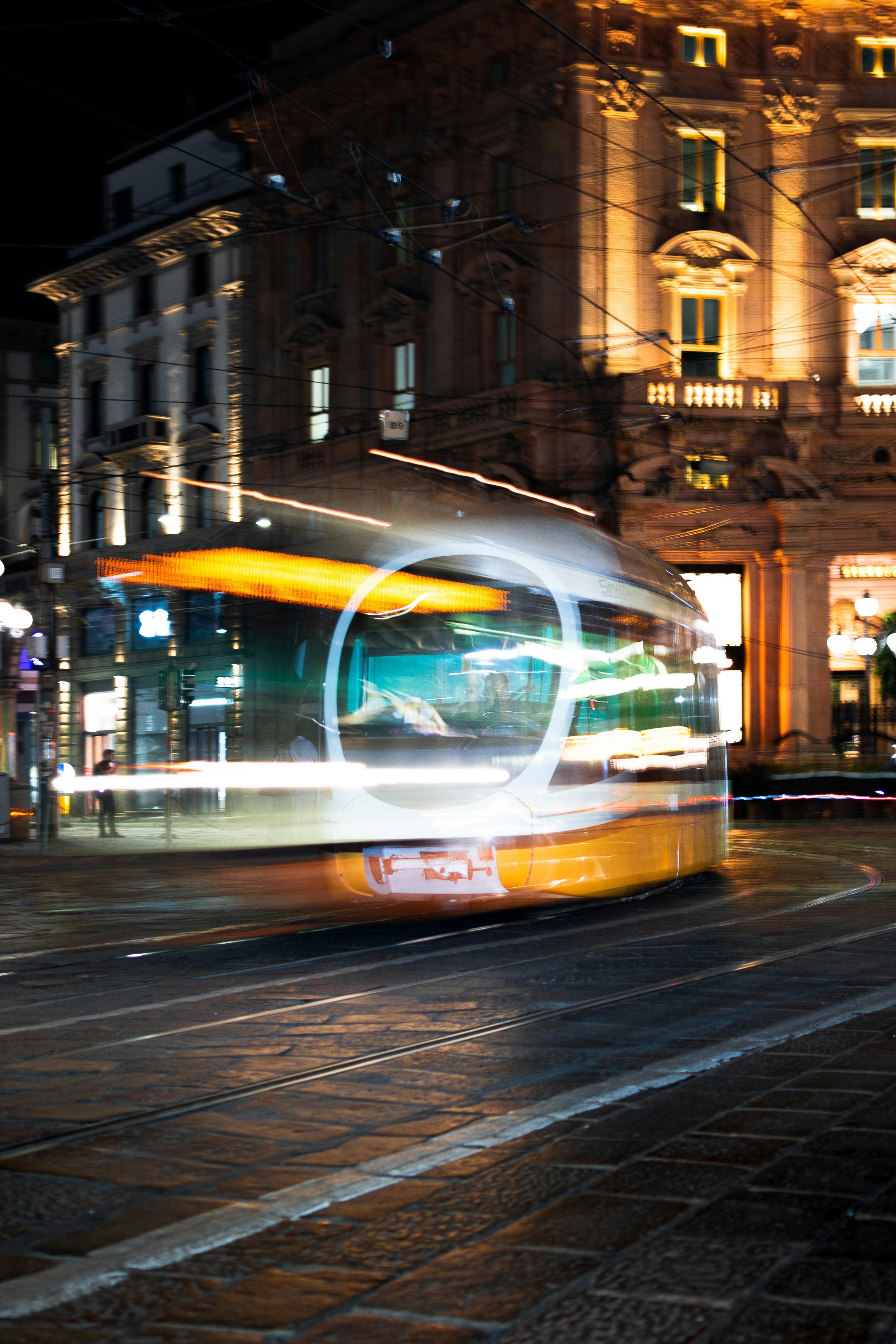 A vibrant tram in motion blurs through a bustling city street illuminated by night lights, showcasing the dynamic energy of urban life.