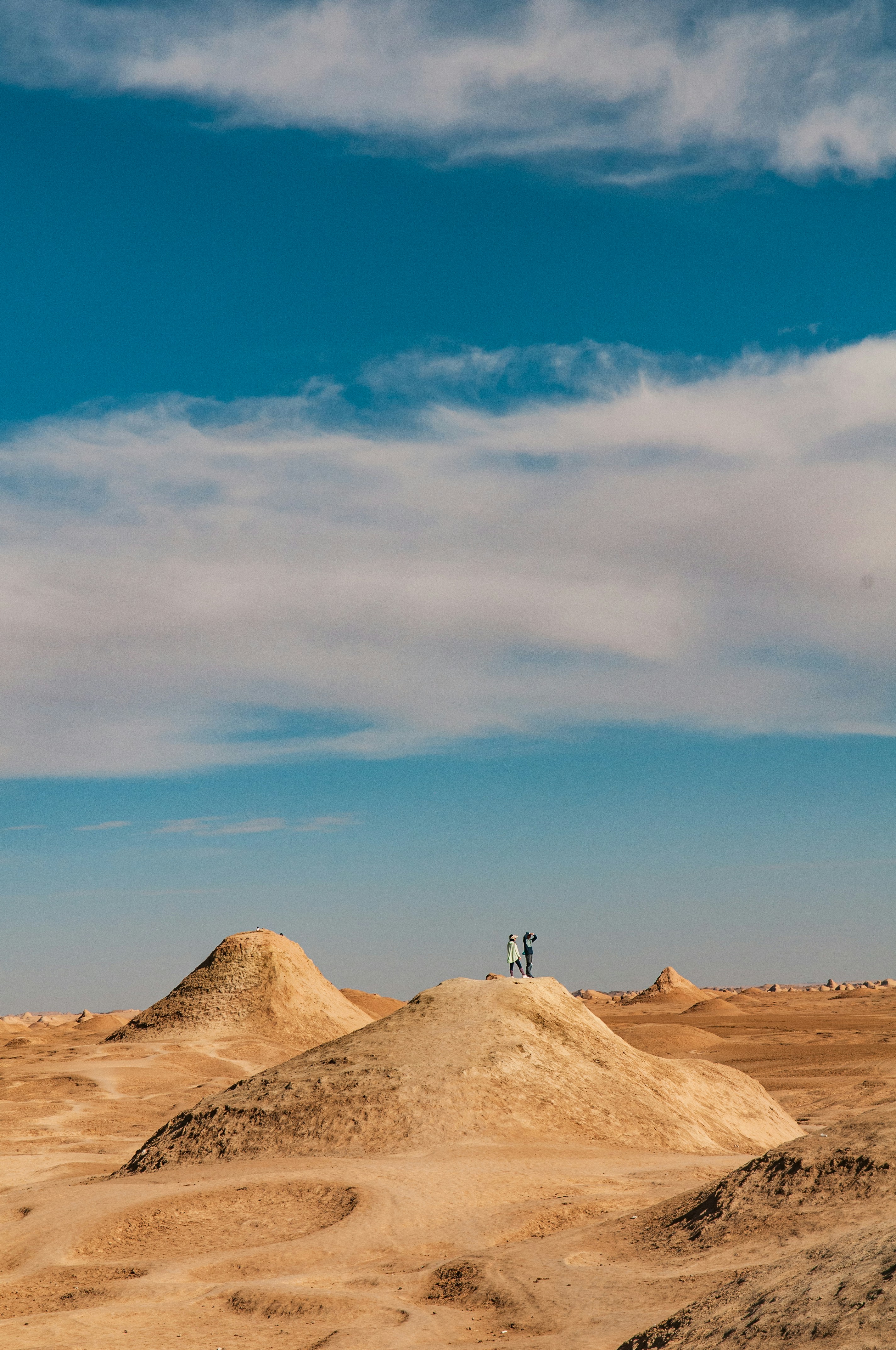 Two Explorers atop Conical Dunes Under a Wide Desert Sky