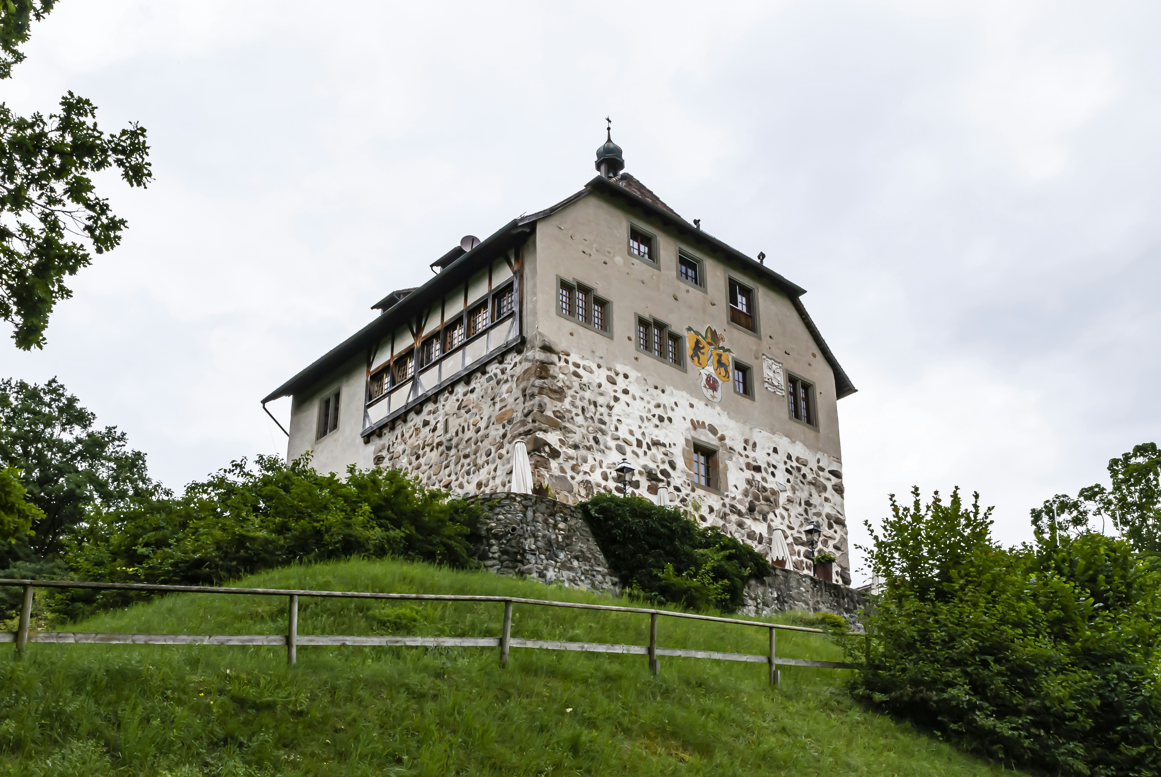 Oberberg Castle perched on a green hill with stone and plaster walls under a cloudy sky.