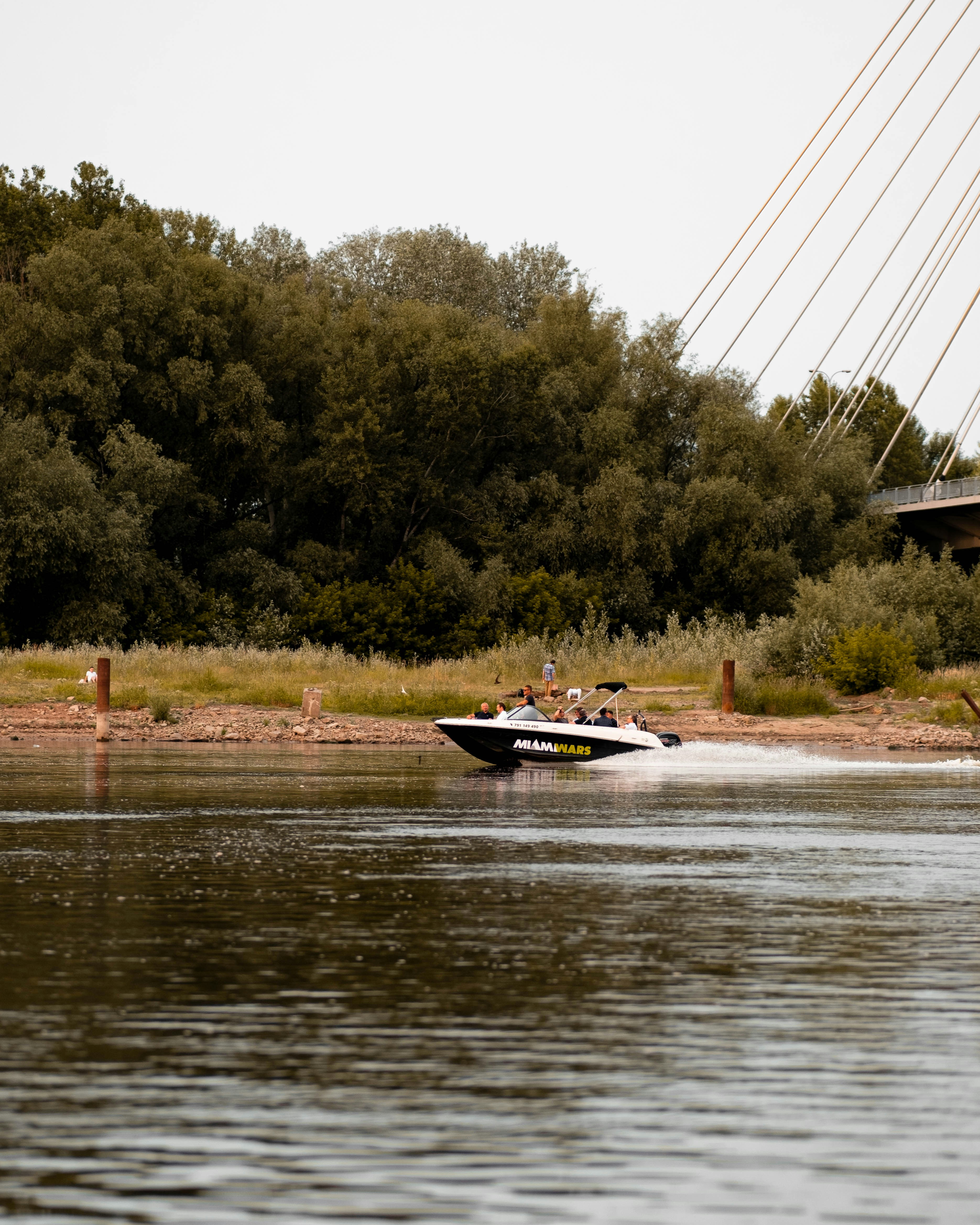 Speedboat slicing through calm waters near a lush riverside, framed by a modern bridge in the background.