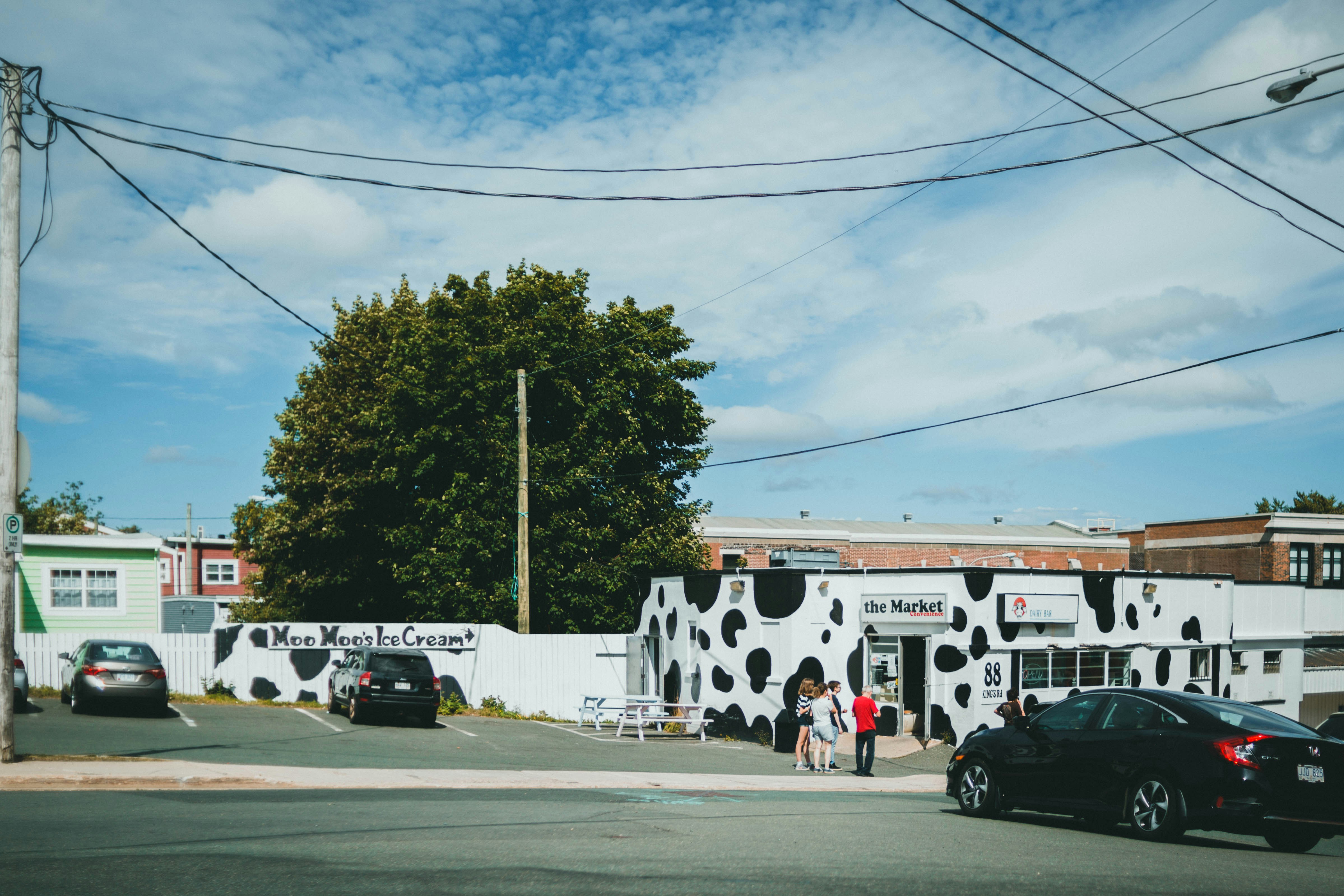 Moo-Marketscape: People at a Cow-Spot Facade Amid a Clear Afternoon