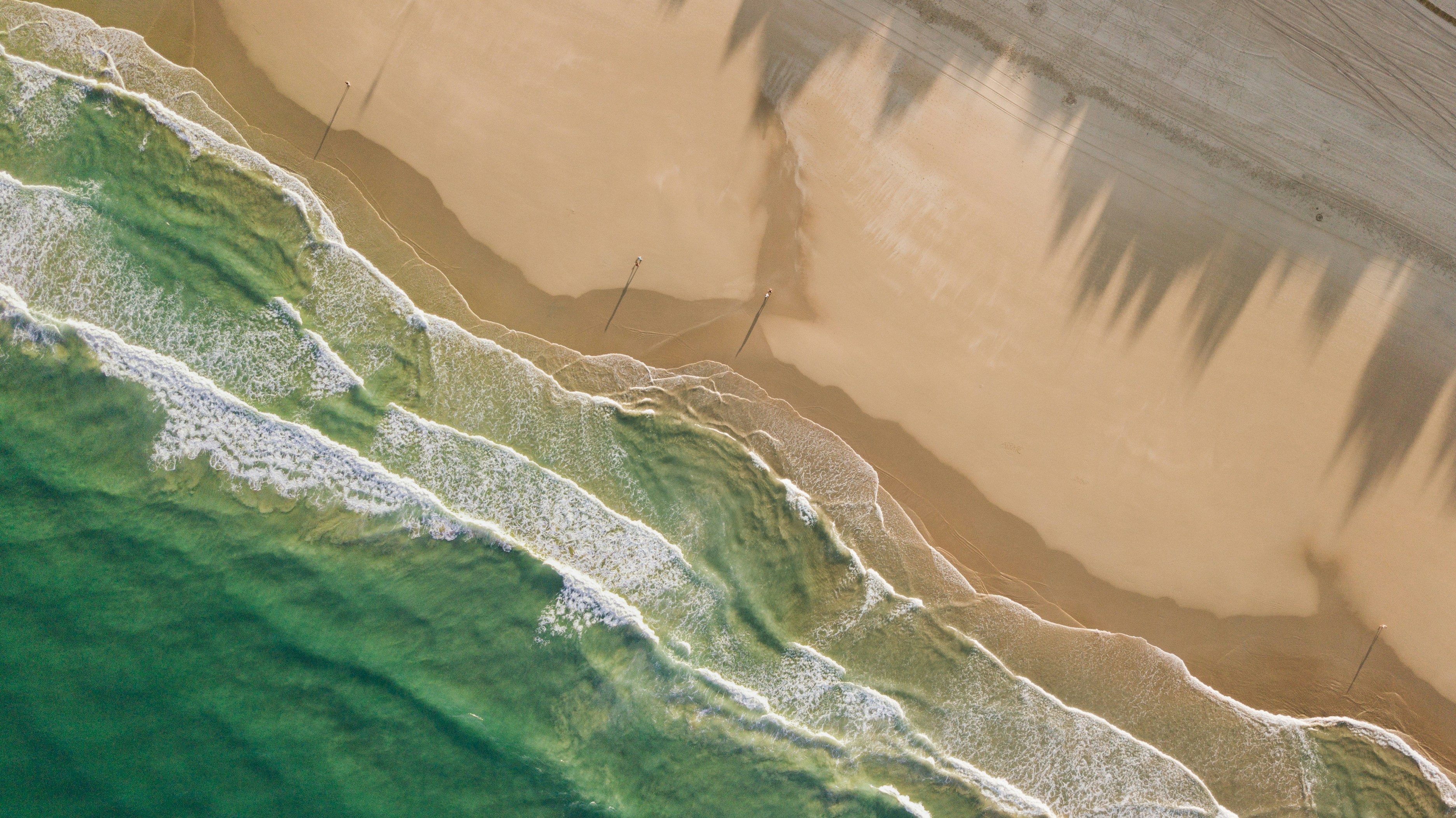 Aerial view capturing the gentle interplay of ocean waves and sandy beach, highlighting the textures and colors of nature's canvas.