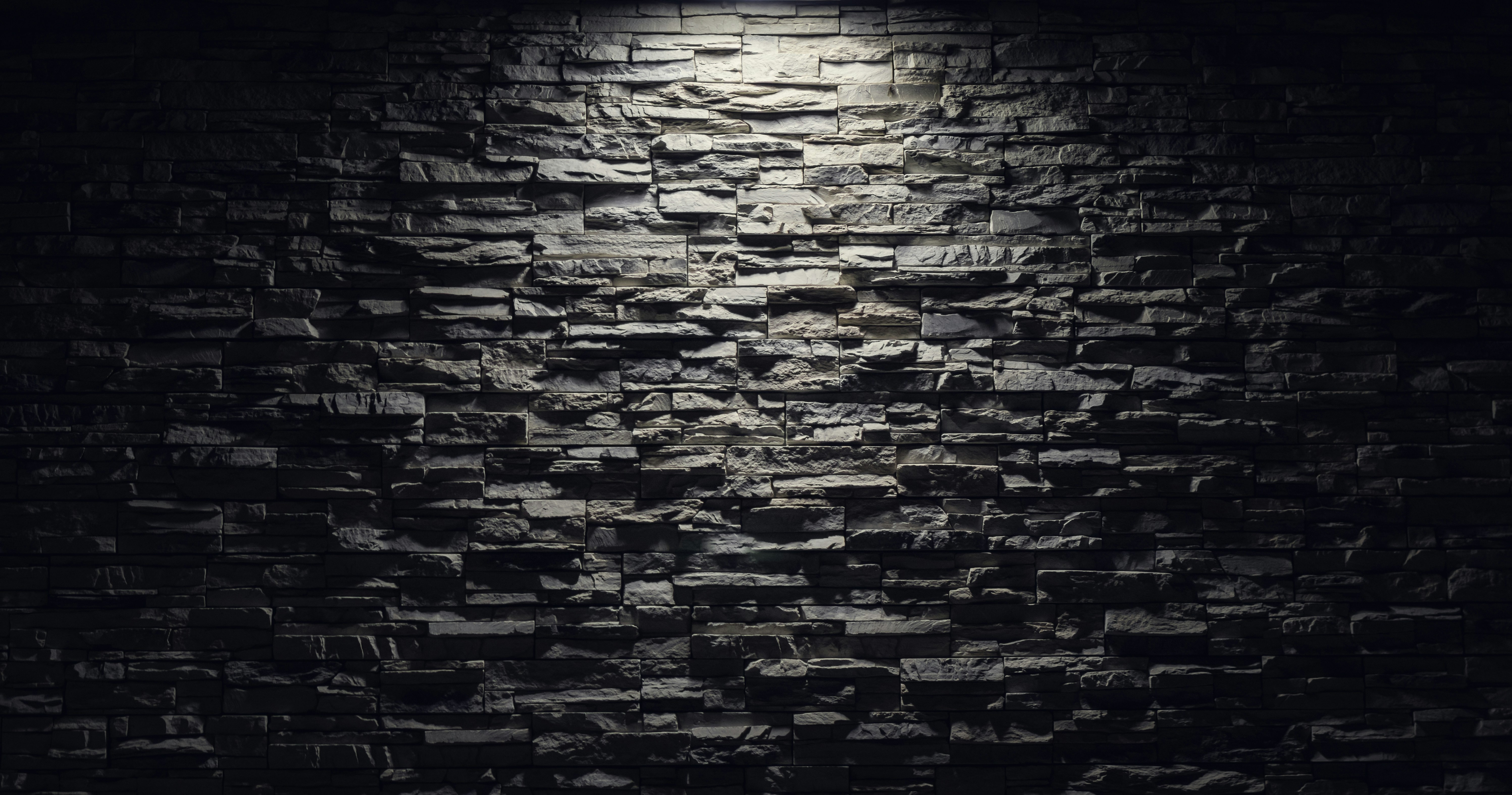 Textured stone wall illuminated by a single overhead light, highlighting the intricate patterns and shadows.