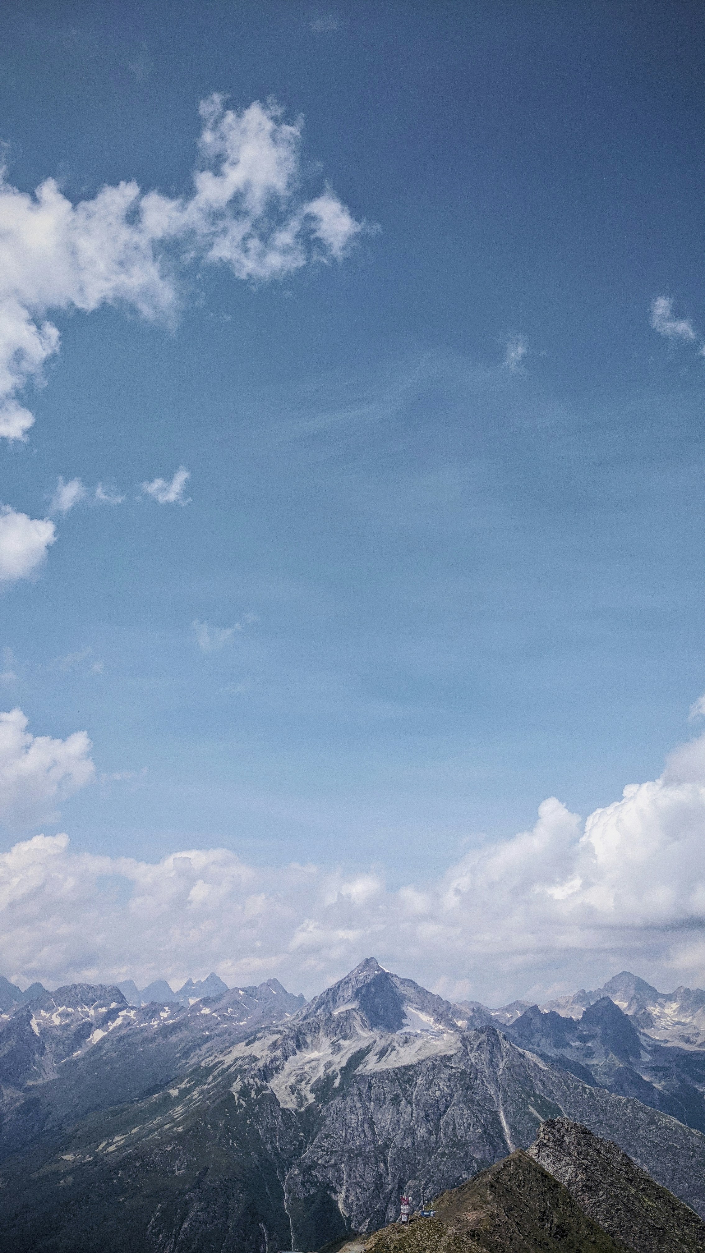 Majestic mountain range under a serene sky, dotted with fluffy clouds and rich textures of rock and greenery.