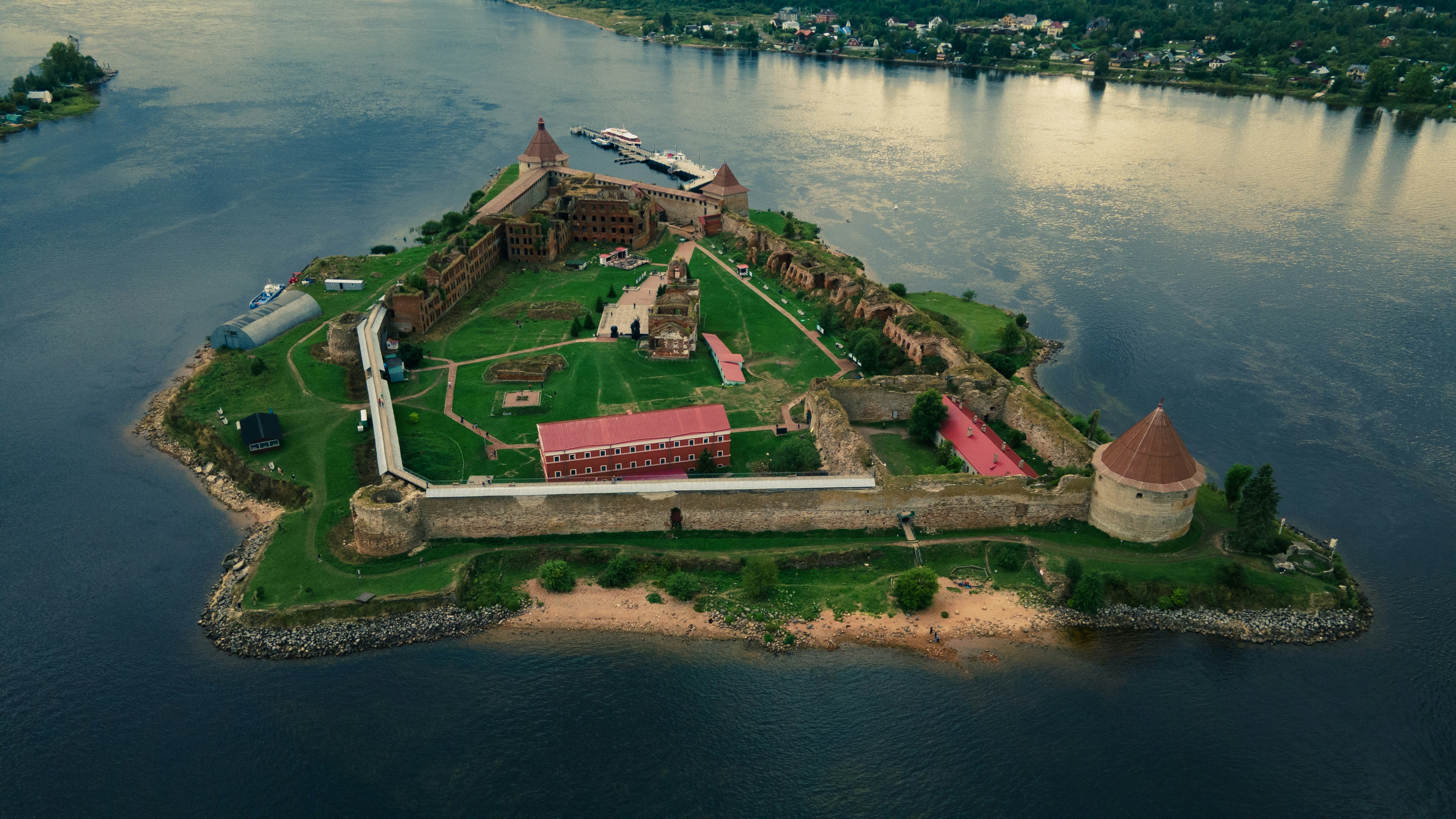 Historic fortress surrounded by serene water with lush greenery and sandy shores.