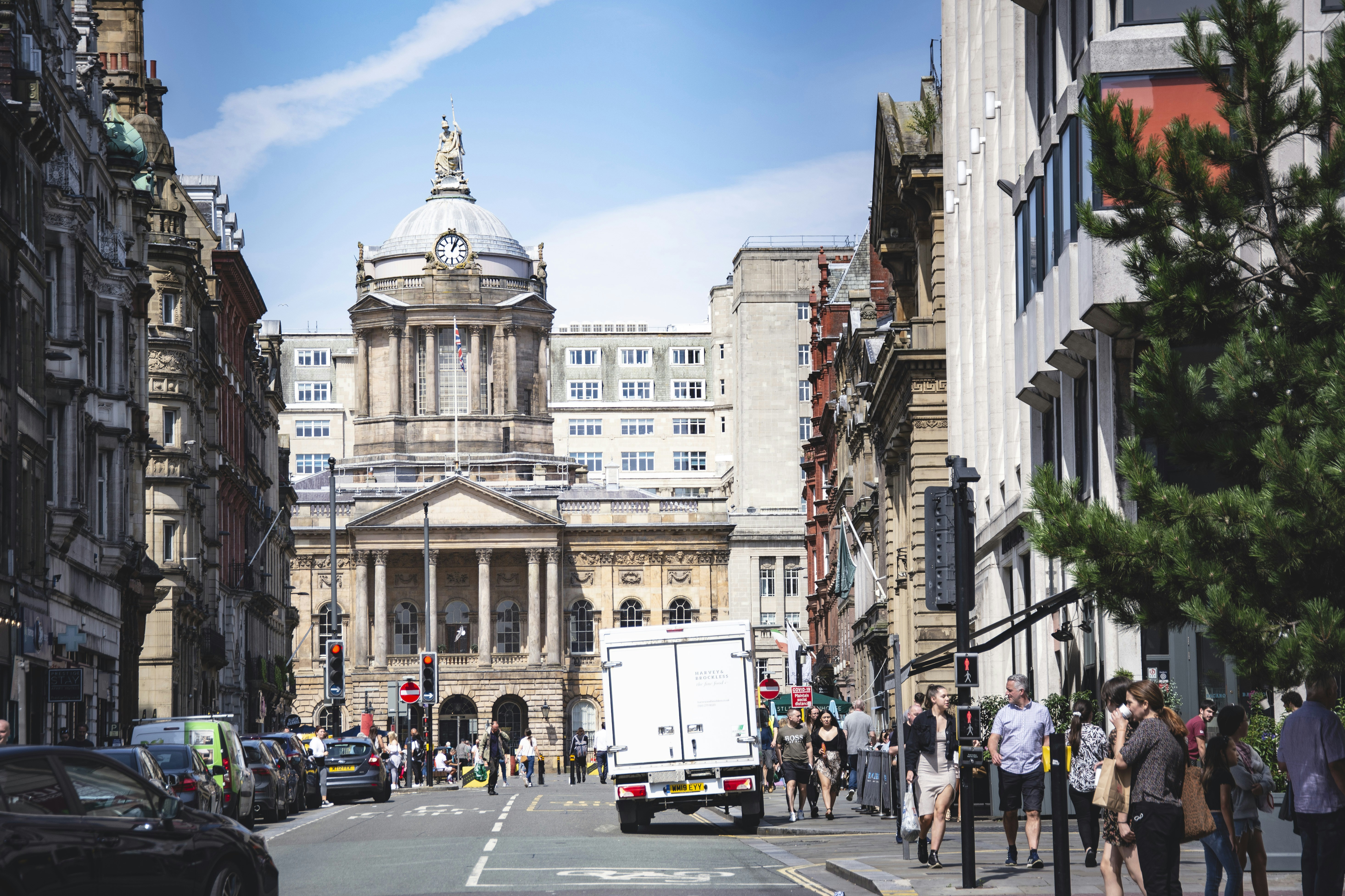 Historic building framed by lively street with pedestrians and vehicles on a sunny day.