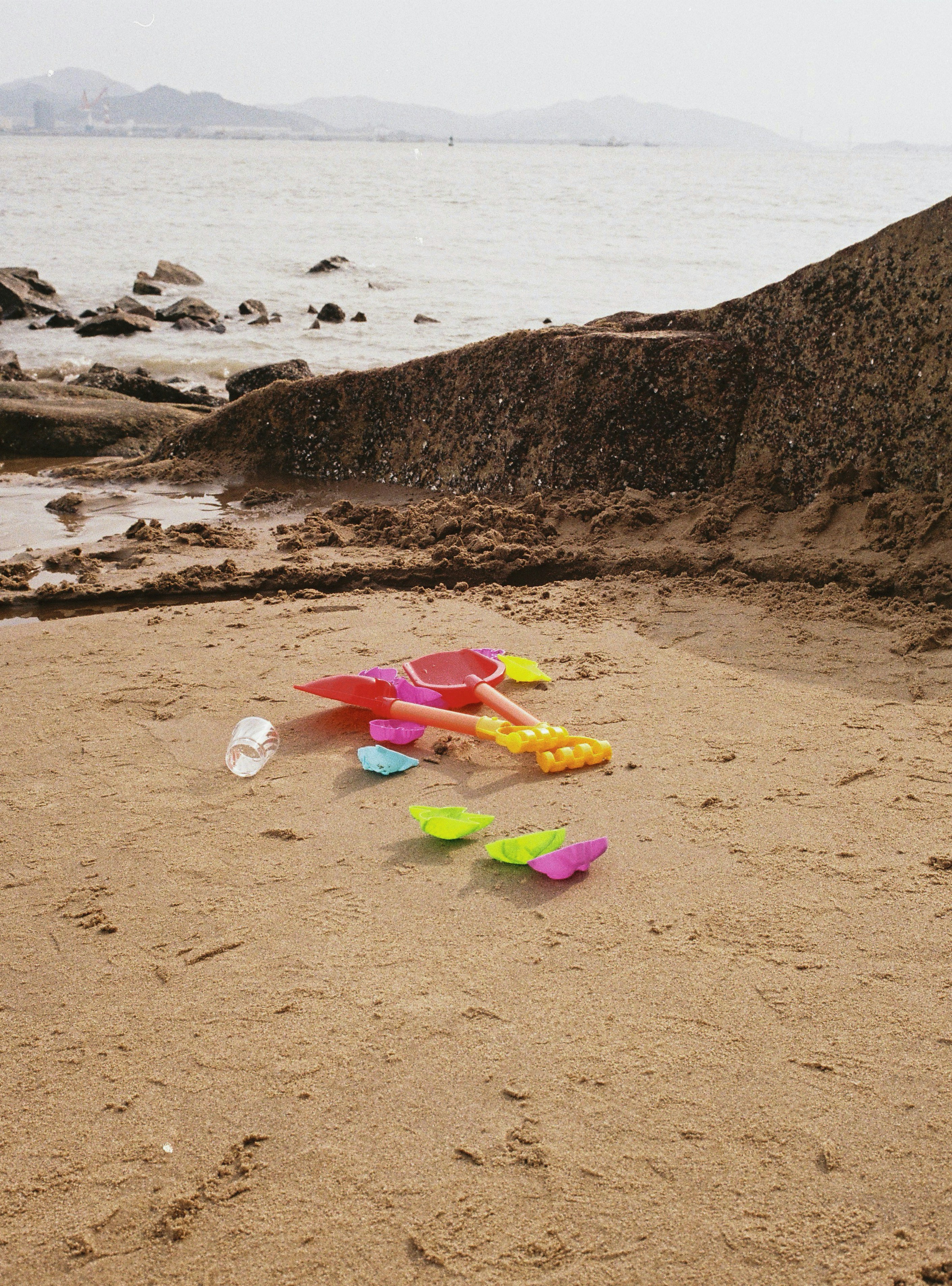 Brightly colored beach toys scattered on sandy shore near the water's edge, evoking a sense of playful summer days.