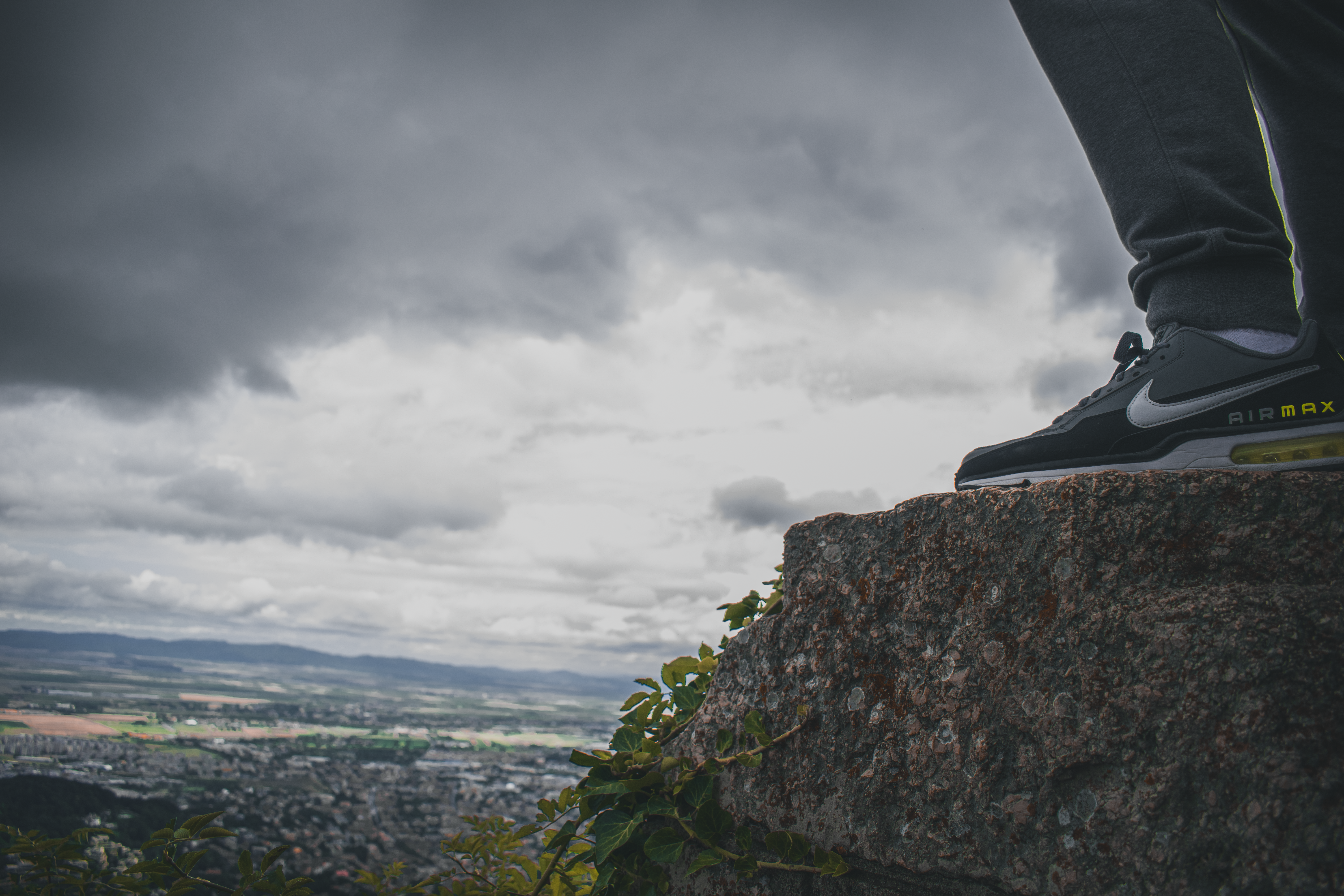 Sneakers on a stone ledge overlooking a vast landscape under a cloudy sky.