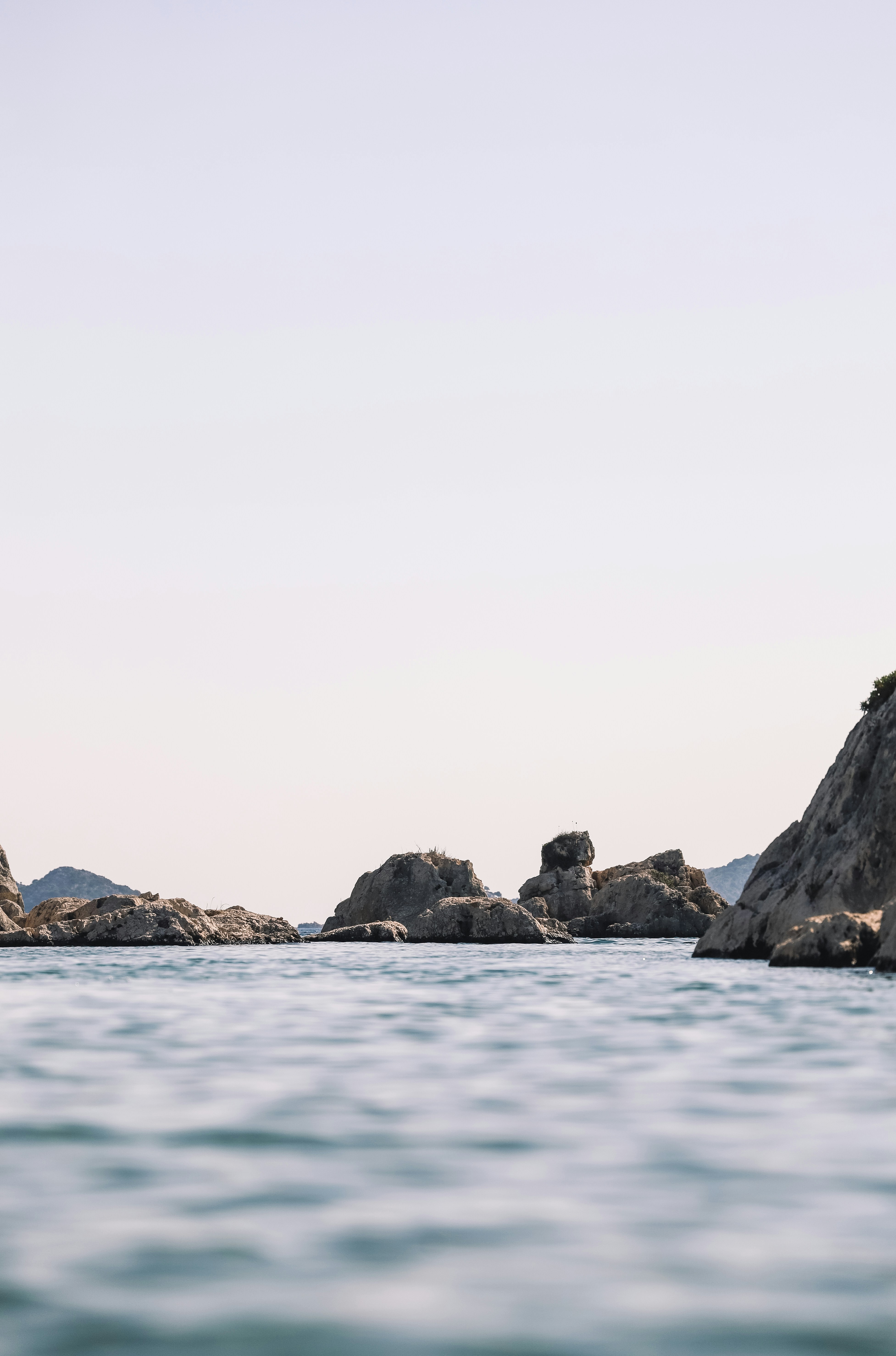 Gentle waves lap against rugged rocks under a soft pastel sky, evoking a sense of calm and tranquility.