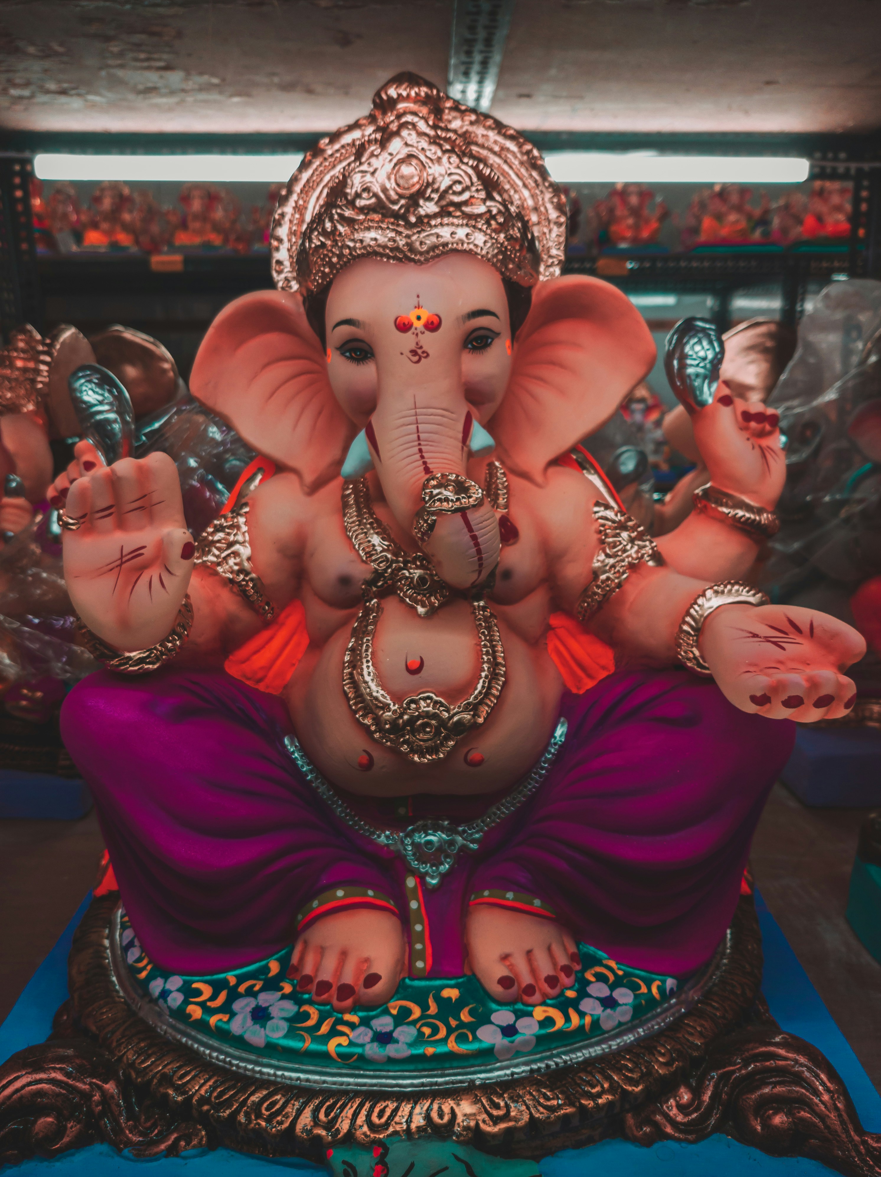 Colorful statue of Lord Ganesha adorned with intricate jewelry and vibrant clothing in a dimly lit setting.