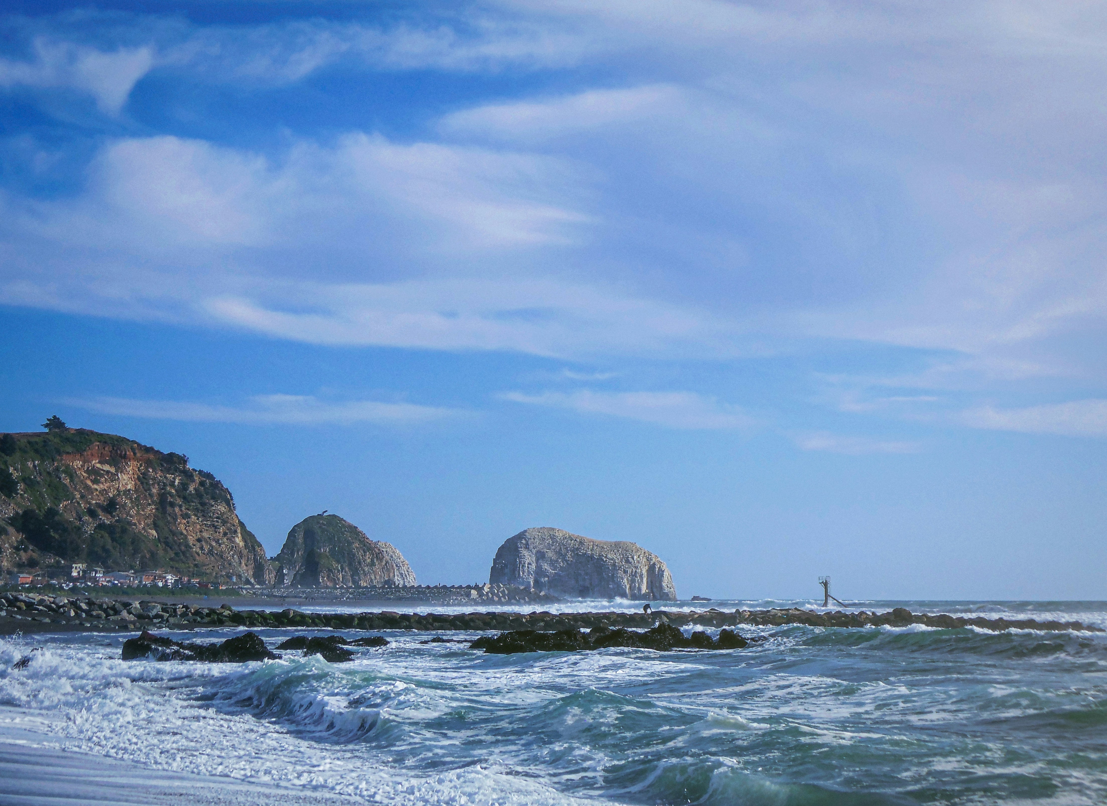 Two prominent rock formations stand guard over a turbulent sea under a vast sky. The dynamic interplay of waves and clouds creates a serene coastal scene.