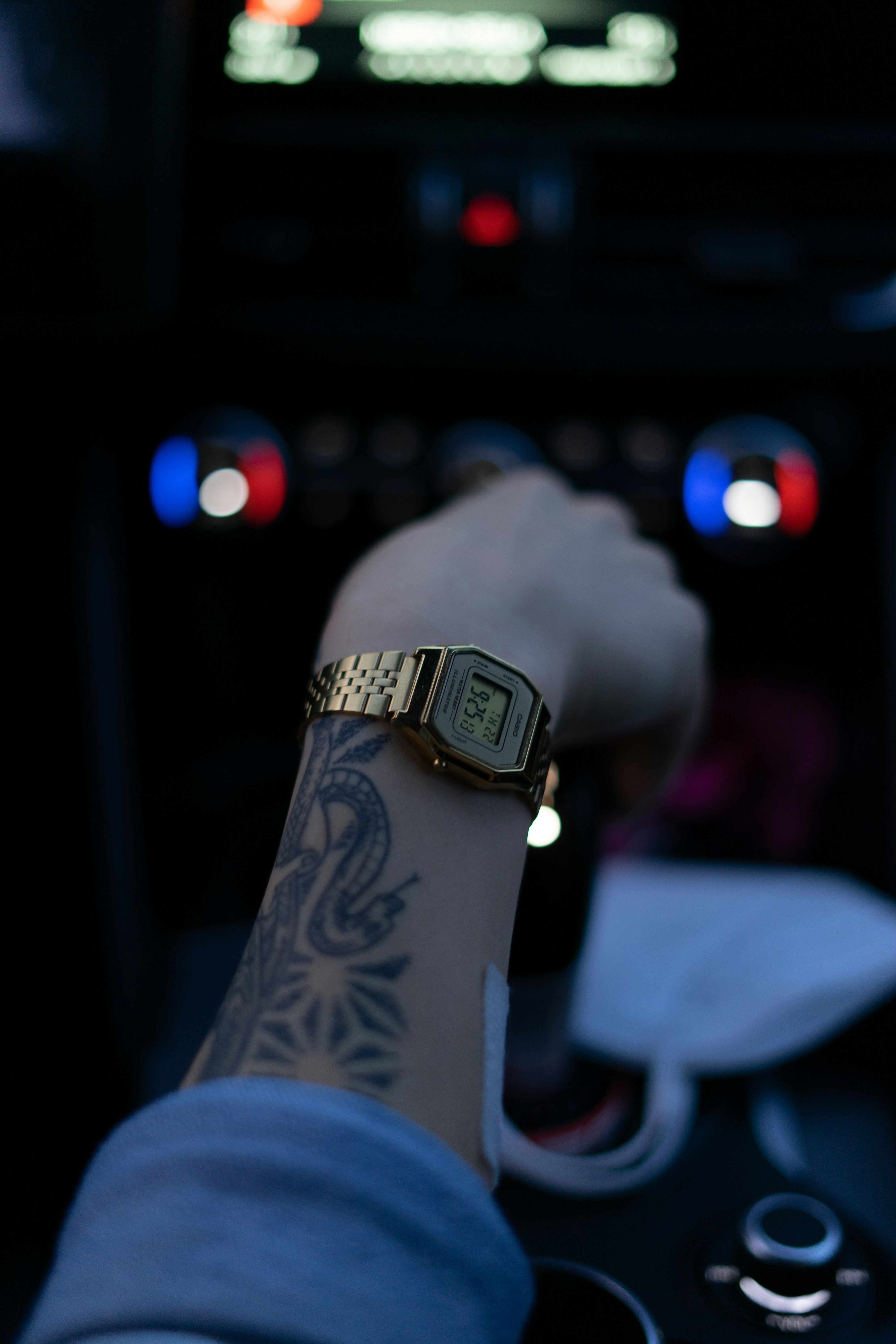 Close-up of a wrist adorned with a gold watch and intricate tattoo, set against the backdrop of a car's interior controls.