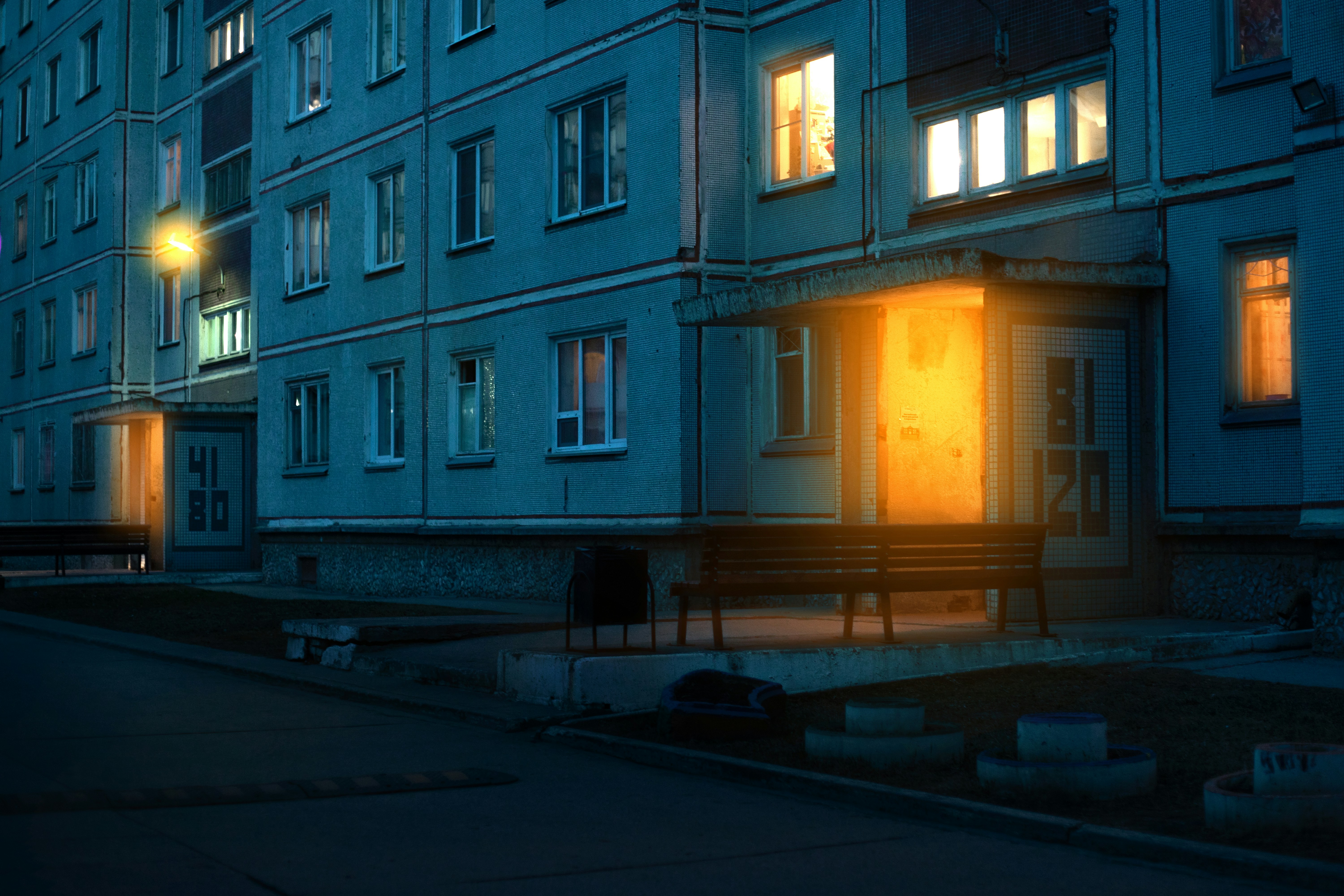 Dimly lit apartment building at night with warm light spilling from doorways, highlighting urban architecture and solitude.