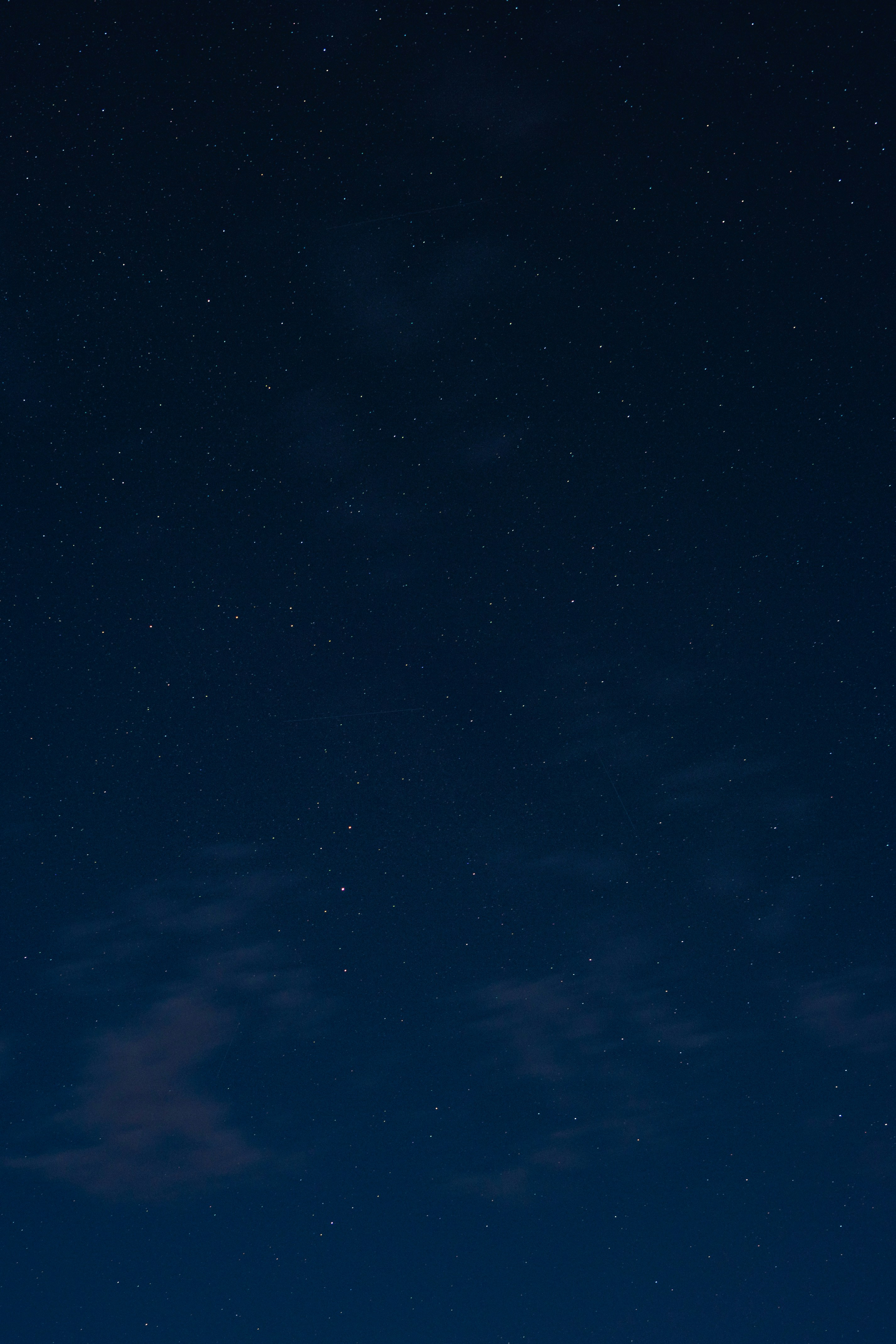 Vast night sky filled with countless stars twinkling against a deep blue backdrop, punctuated by subtle wisps of clouds.