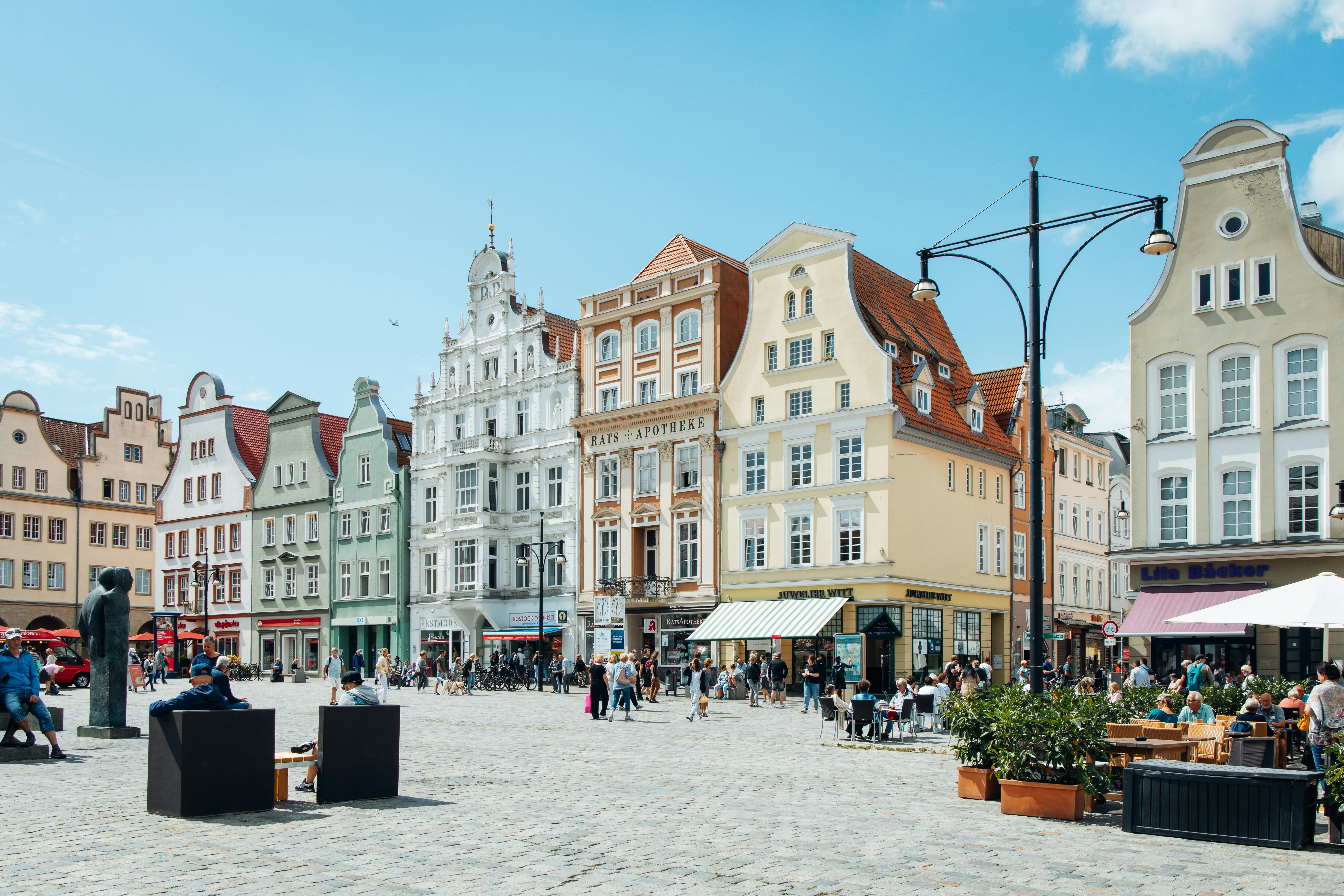 Colorful historic buildings line a bustling European town square under a clear blue sky.