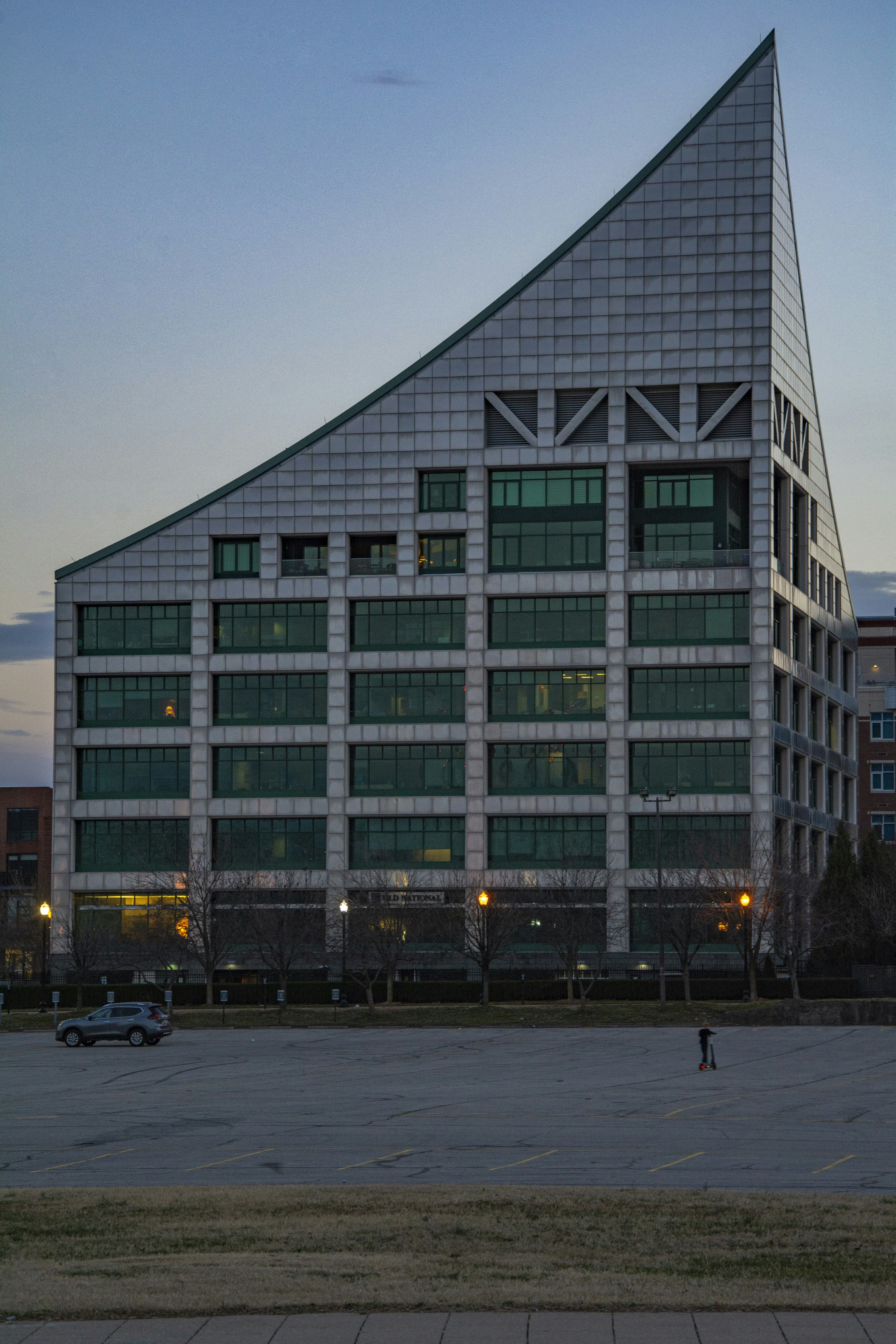 Contemporary building with a distinctive sloped roof and large glass windows, set against a twilight sky. The scene captures the interplay of architecture and evening light.