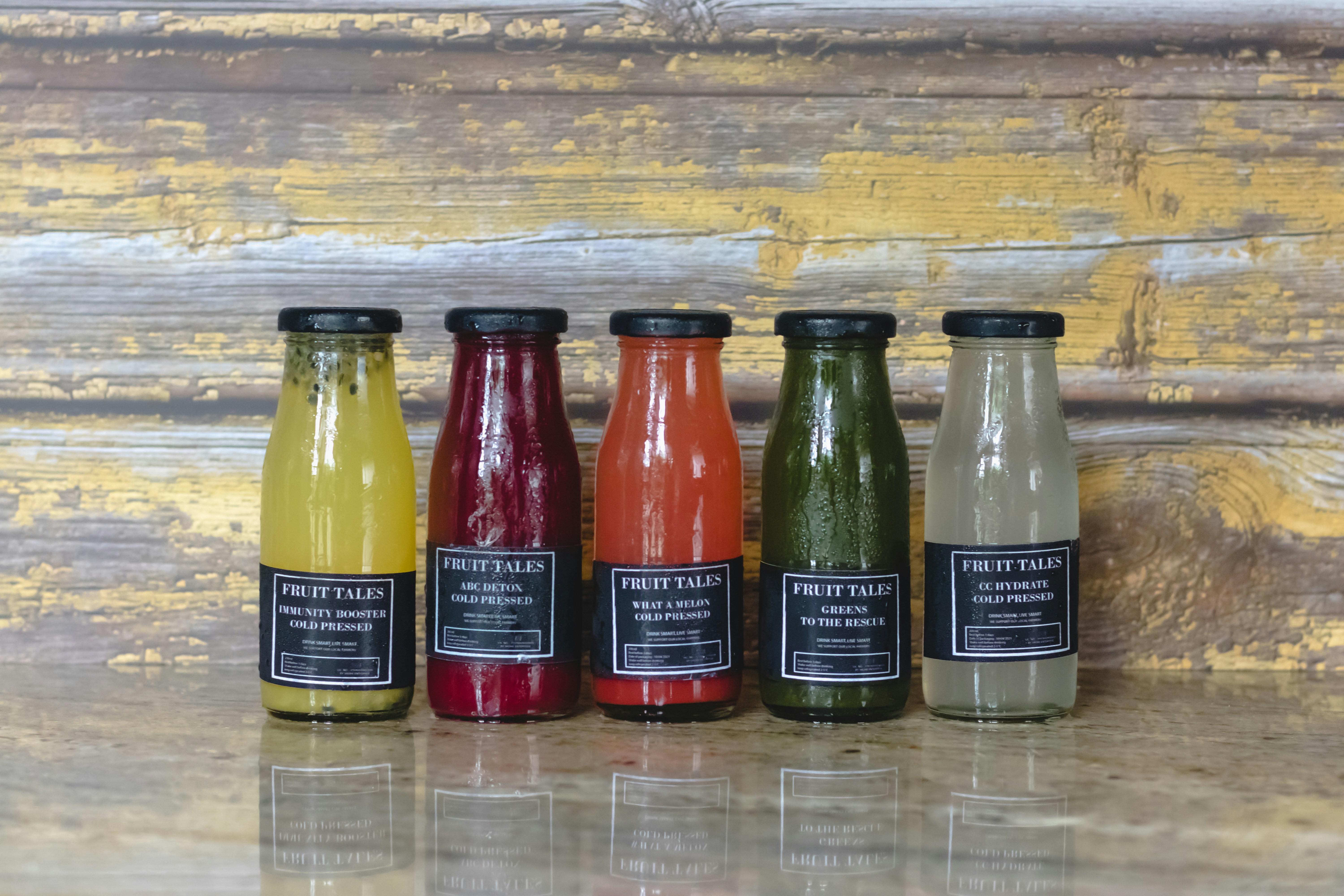 Five colorful juice bottles arranged against a rustic wooden backdrop.