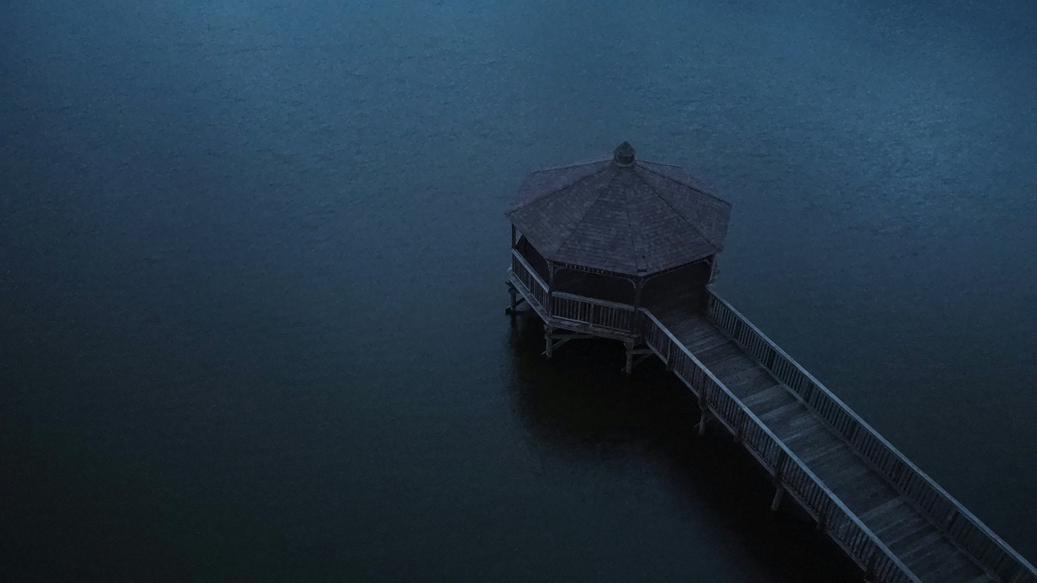 Hexagonal wooden dock extending into a vast, serene body of water under low light.