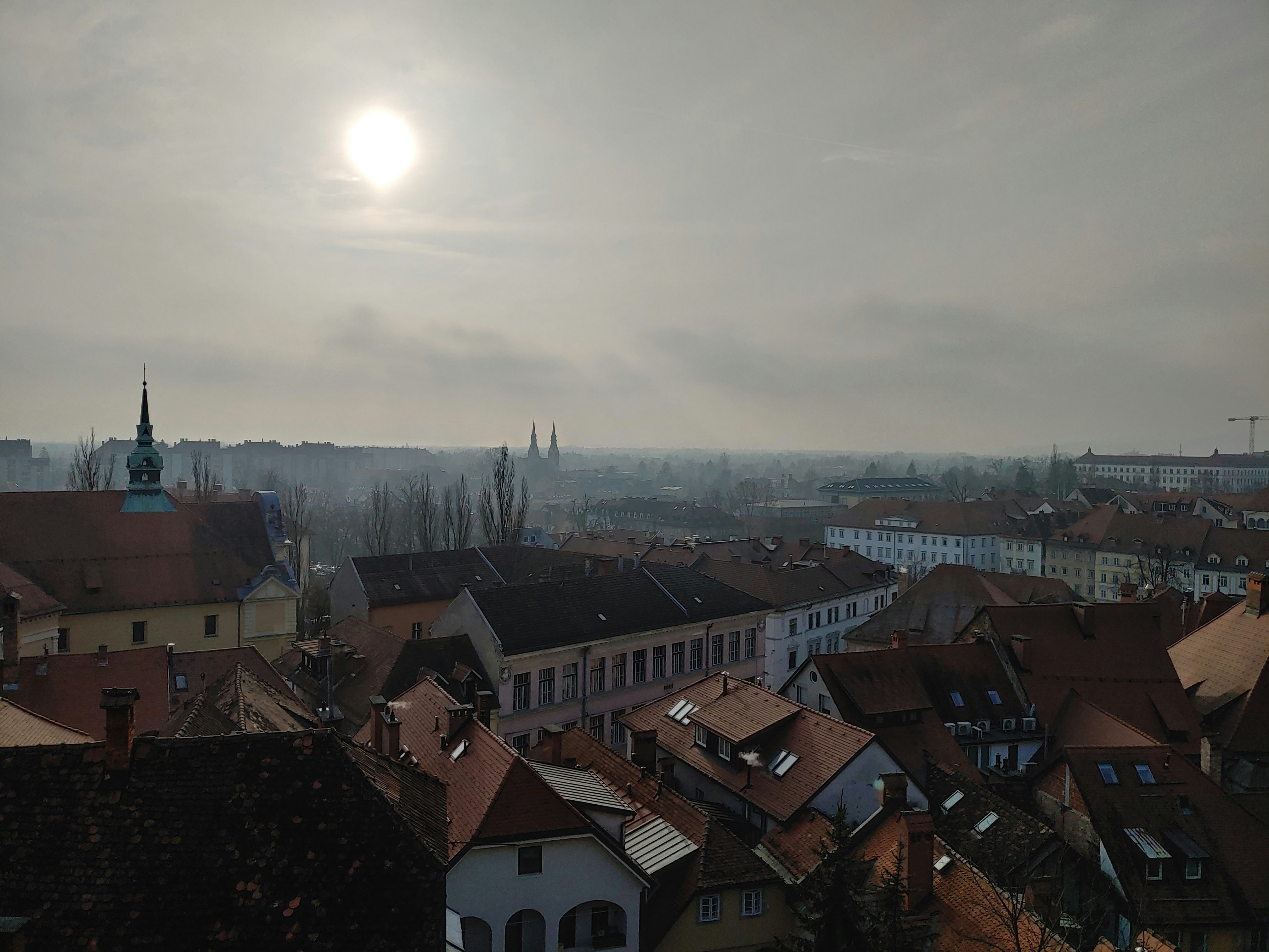Sun peeking through cloudy sky over a cityscape with historic buildings and church spires.