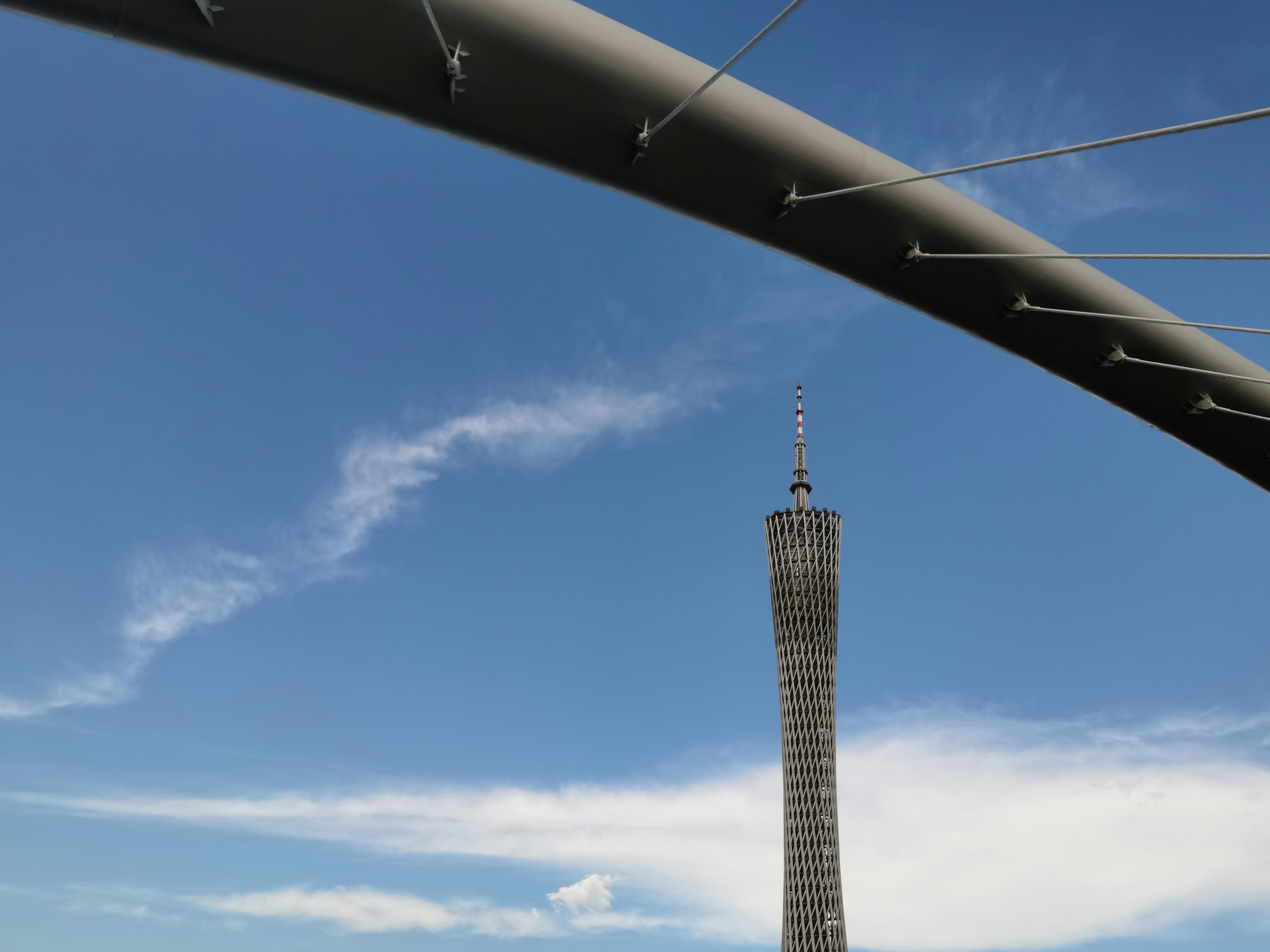 Tall tower framed by a curving bridge against a clear blue sky.