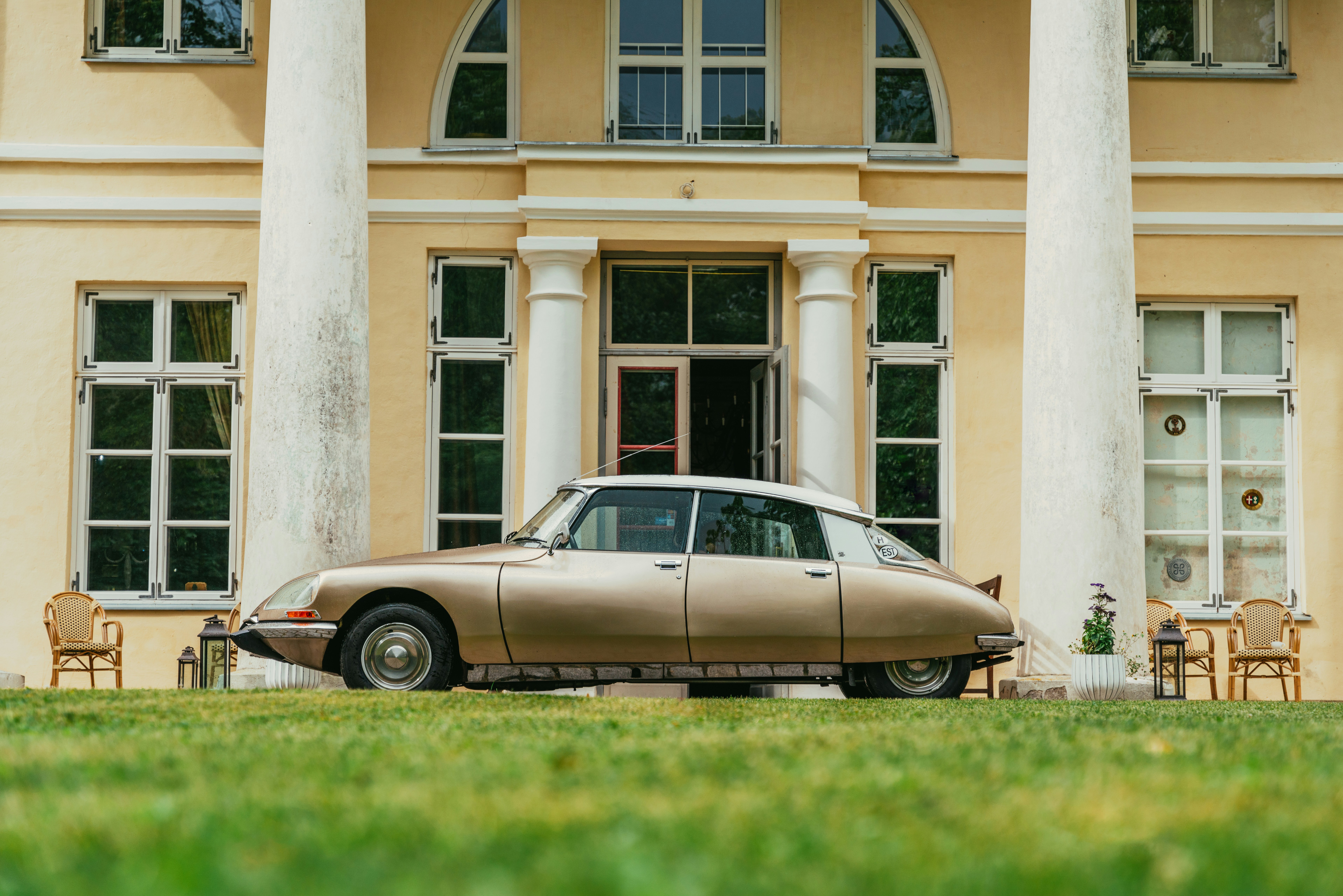 Classic Citroën DS parked in front of a grand building with tall columns and large windows, showcasing a blend of vintage automotive design and architectural beauty.