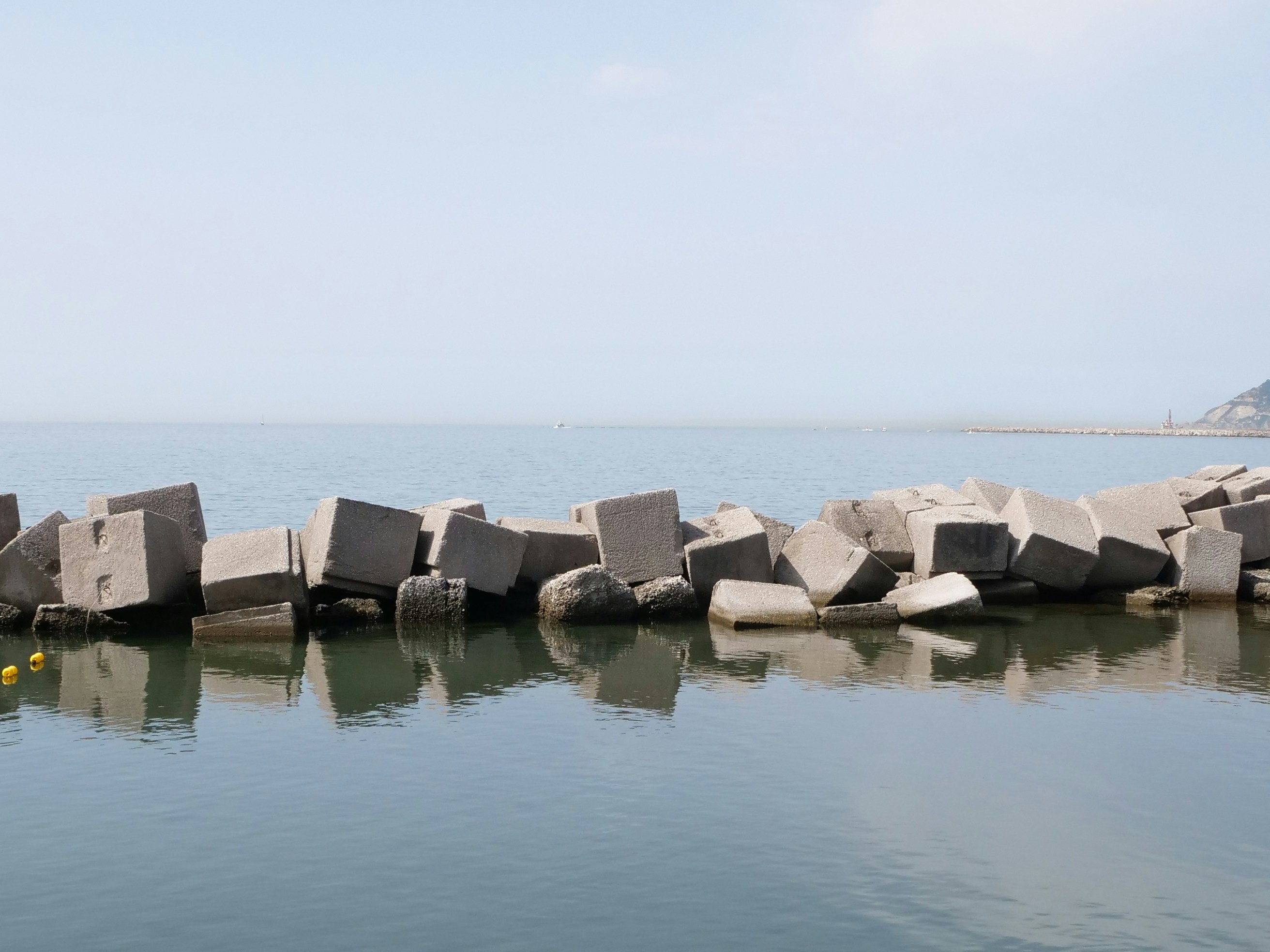 Row of large concrete blocks reflecting in calm water under a clear sky.