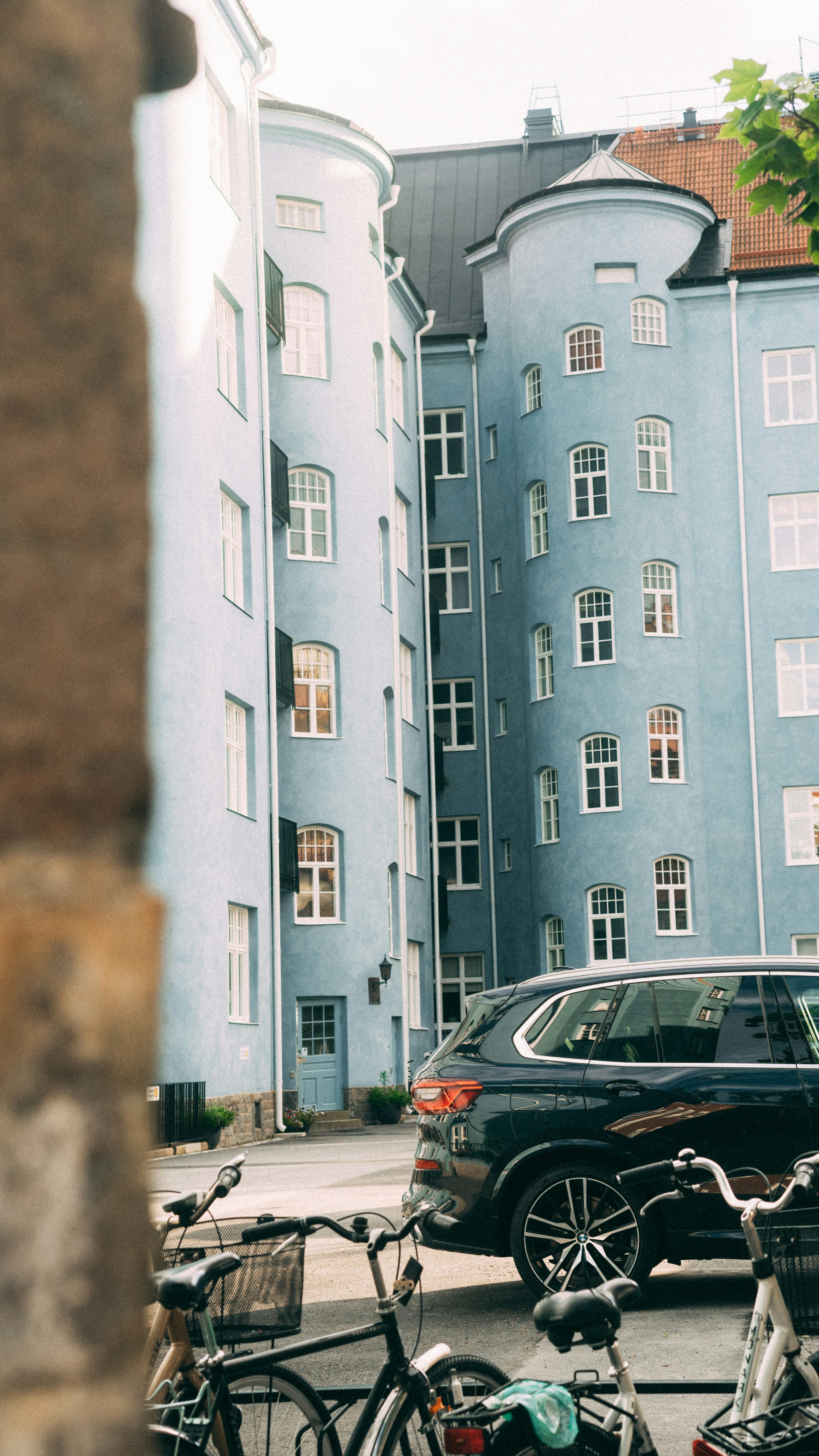 Blue rounded apartment buildings with white-trimmed windows stand beside parked bicycles and a car on a quiet street.