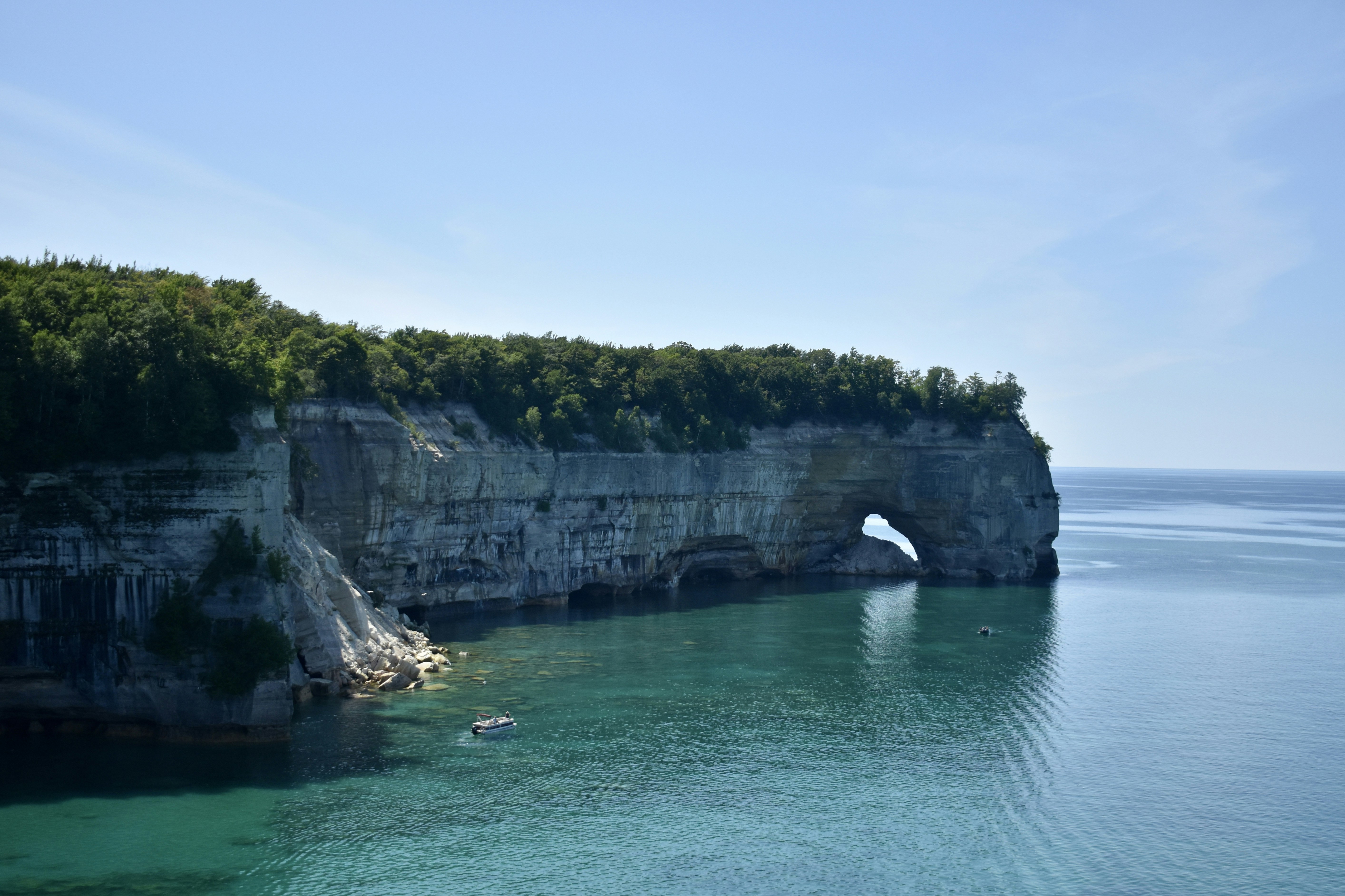A natural rock formation with an arch, surrounded by lush greenery and tranquil waters, showcasing the beauty of the coastline.