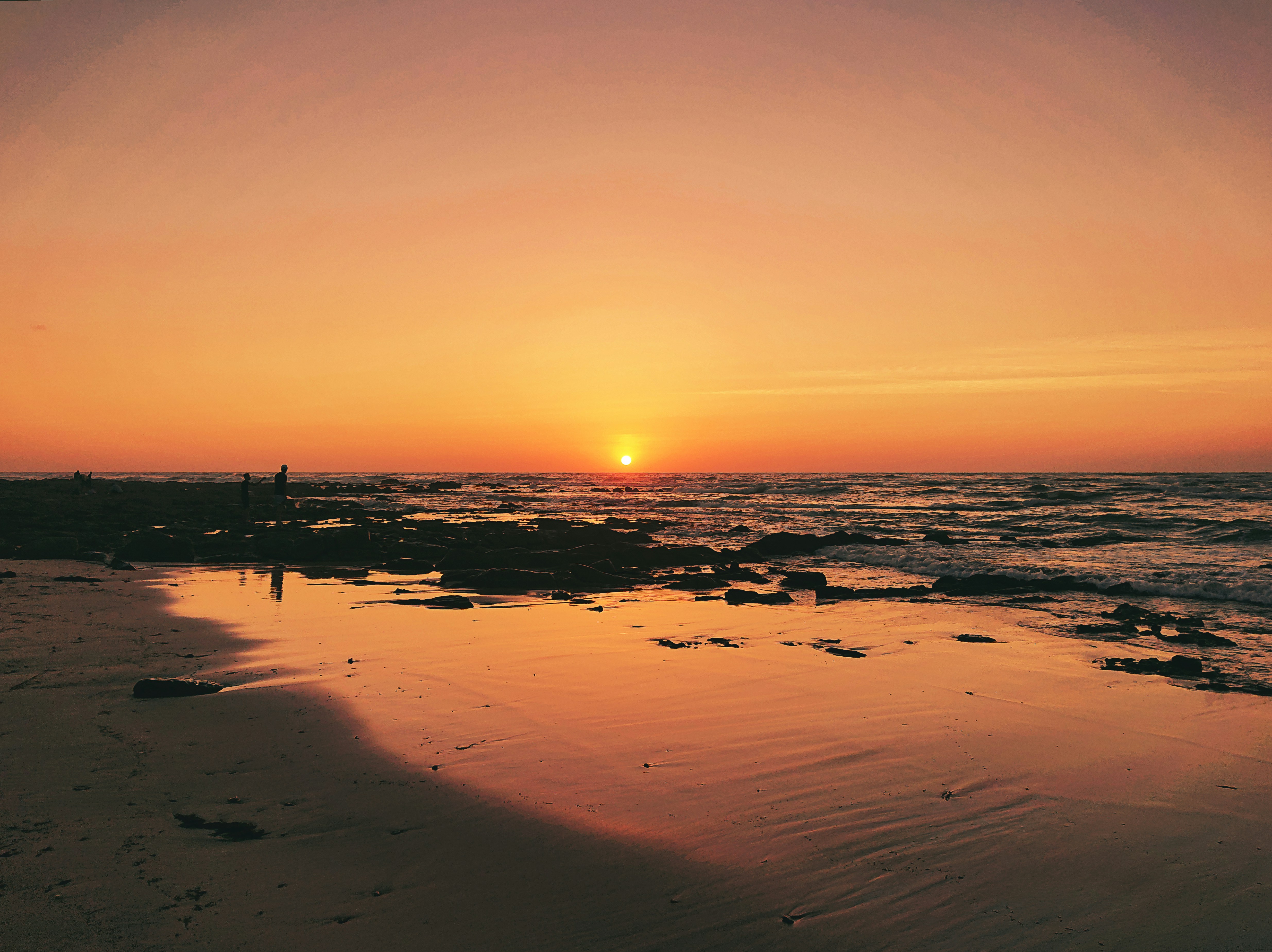 Sunset over a tranquil beach with gentle waves and a warm, glowing sky.