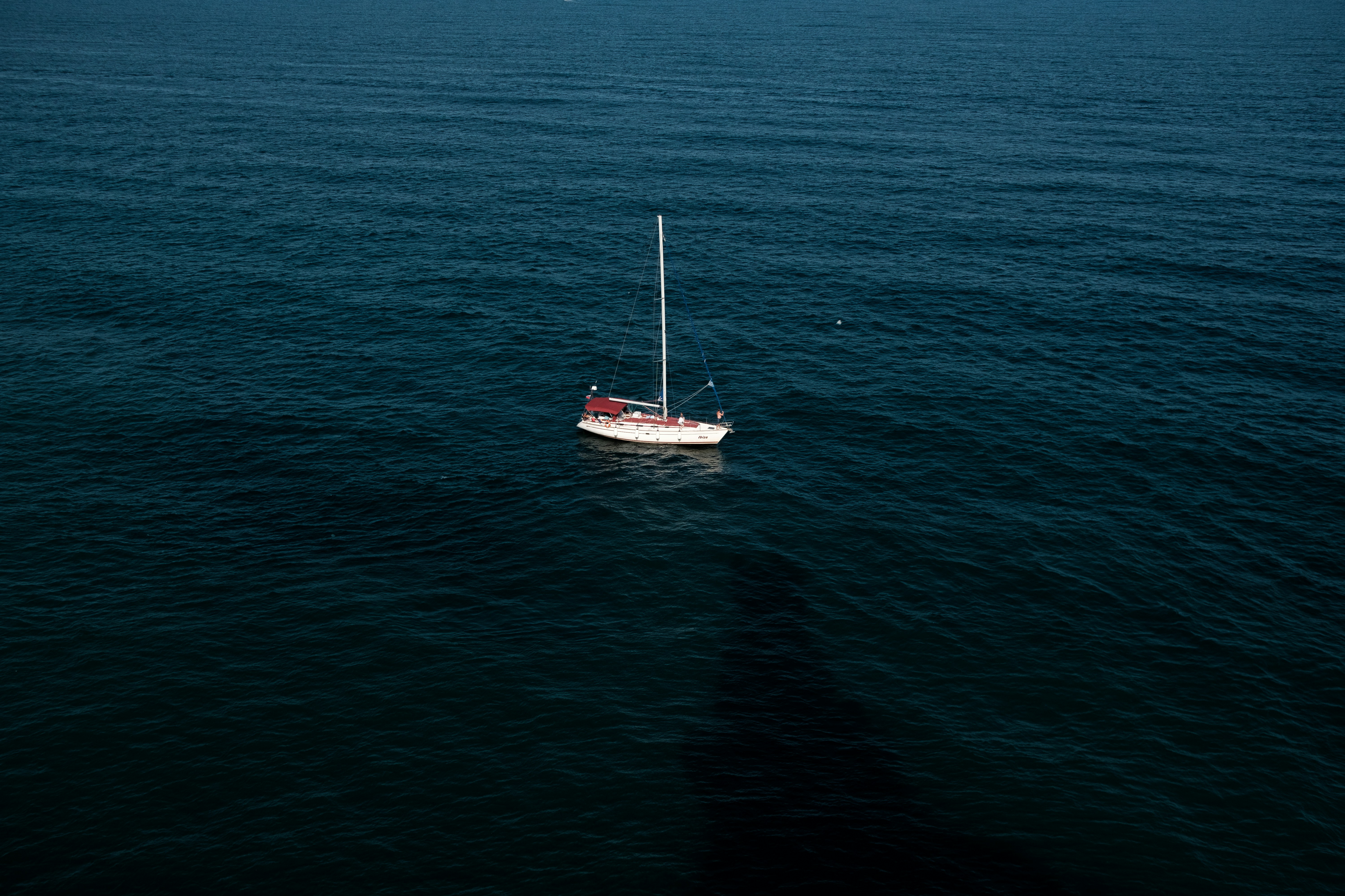 A lone sailboat drifts gracefully across the deep blue sea, casting a gentle shadow on the water's surface.