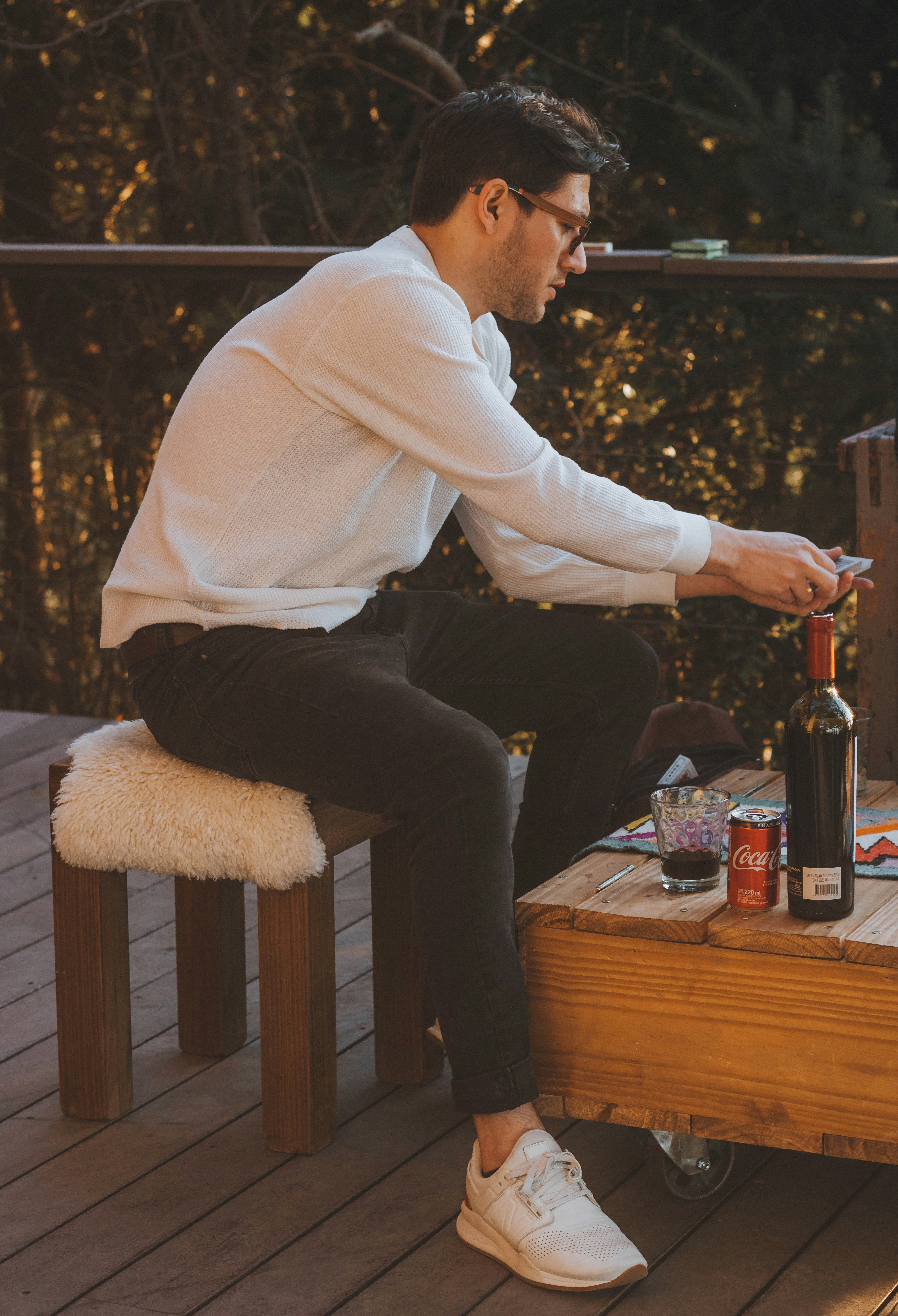 Deckside Pause: Portrait of a man in a white sweater at golden hour with wine and soda on a wooden table