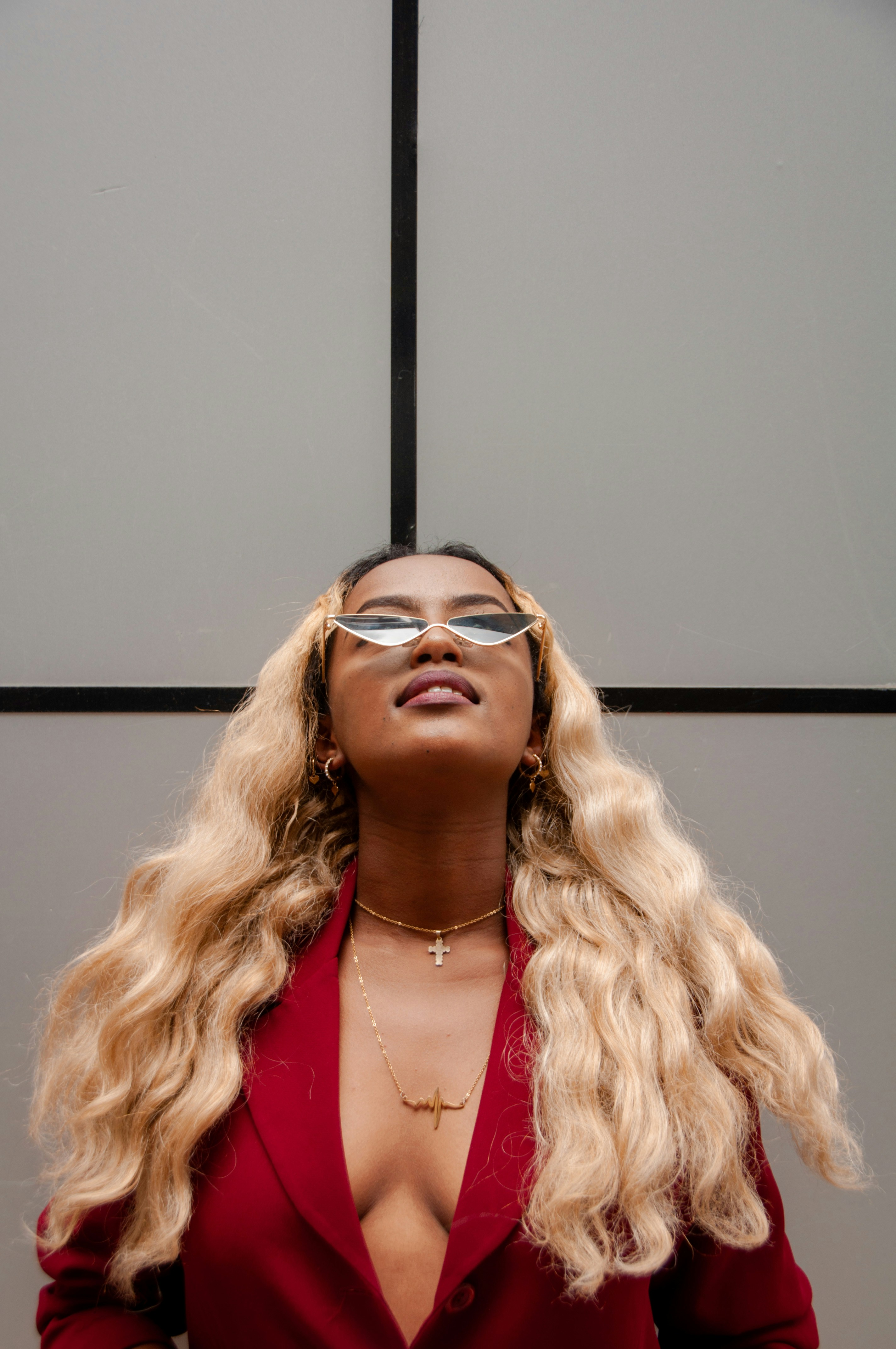 Model gazing upward with stylish sunglasses, dressed in a deep red blazer against a minimalist backdrop.