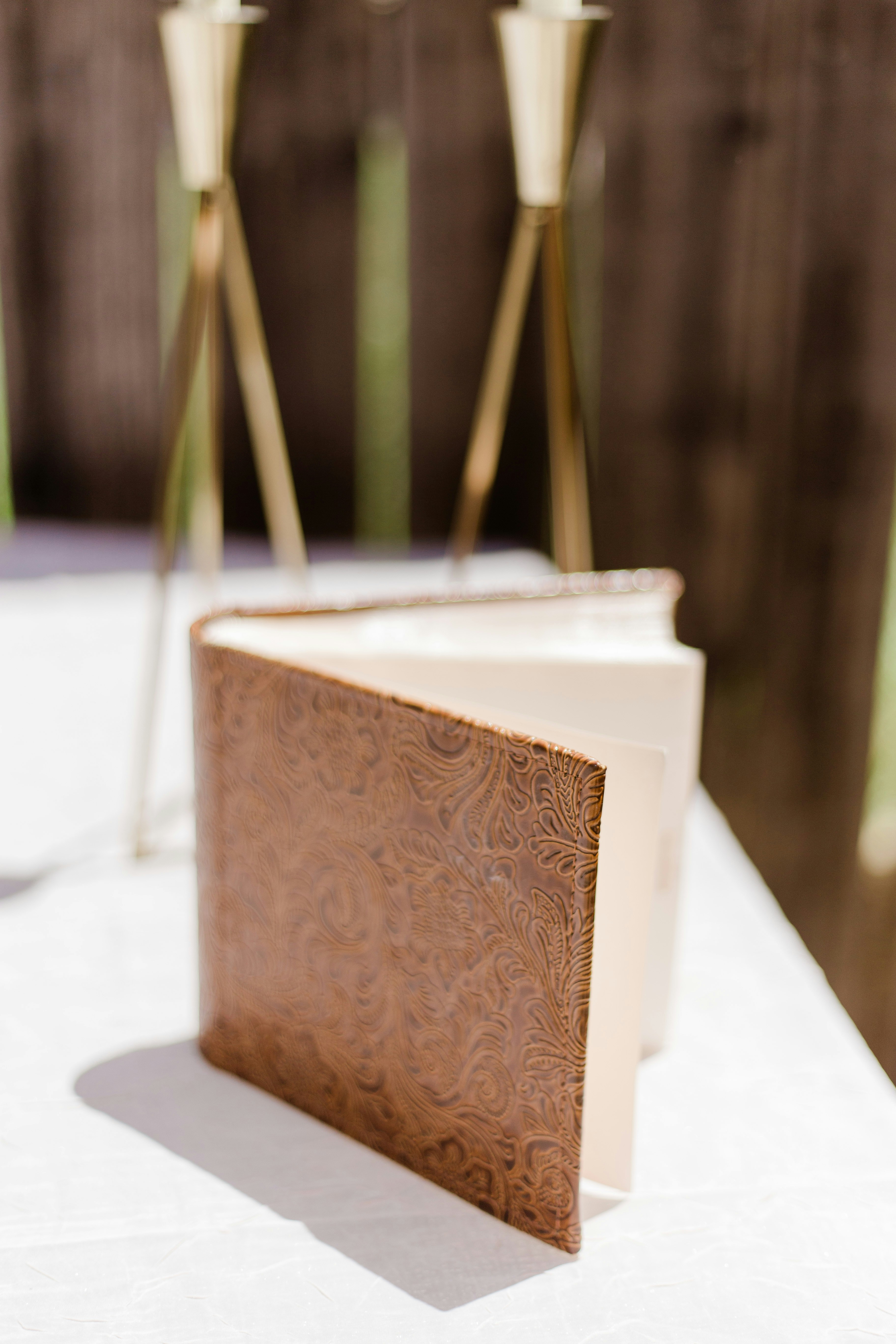 Intricately designed leather journal resting on a table, complemented by elegant candle holders in the background.