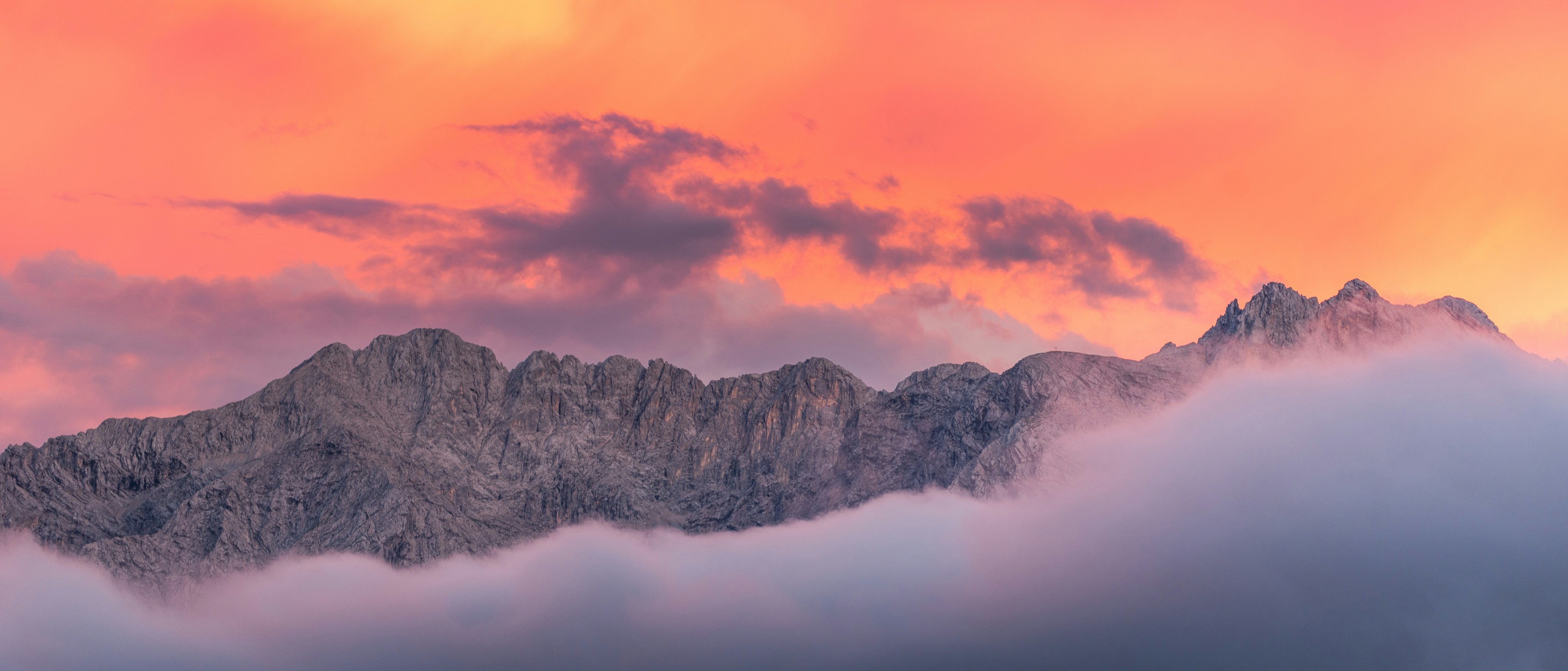 Rocky mountain peaks beneath vibrant orange clouds at sunset.