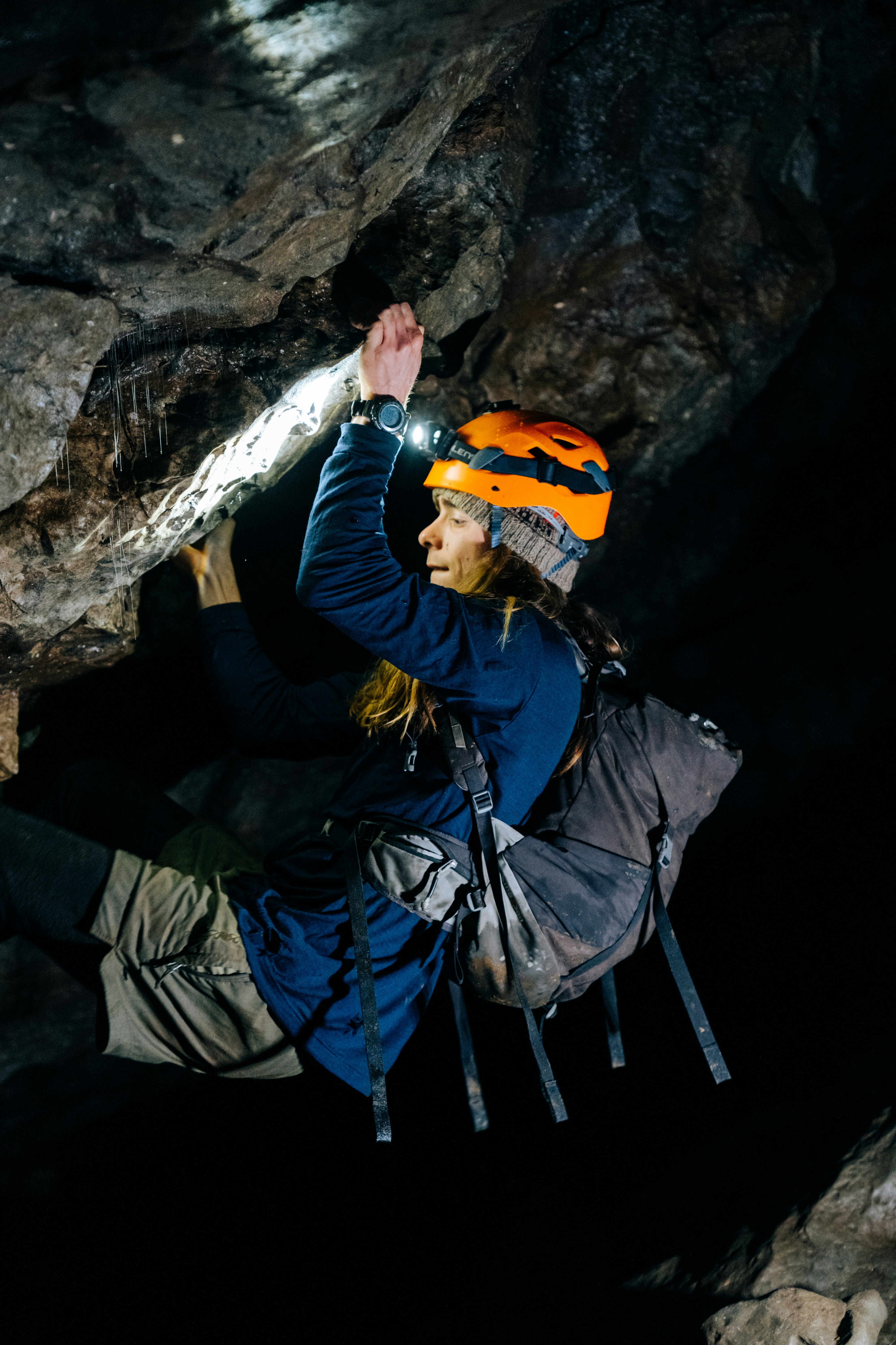 Climber navigating a rocky cave with a headlamp, showcasing determination and skill. The scene captures the essence of adventure in a subterranean environment.