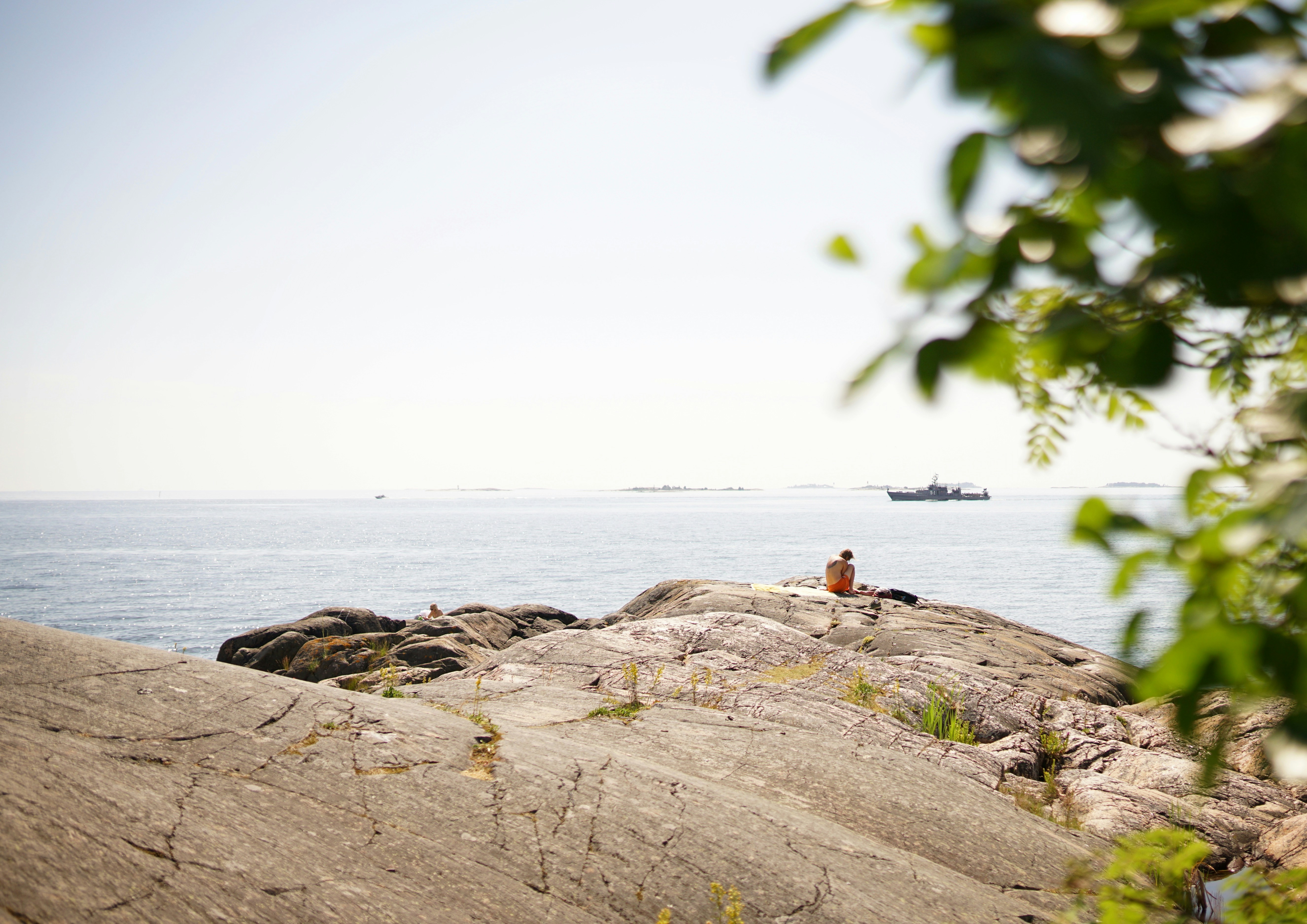Lone Figure on Granite Promontory: Quiet Sea and a Distant Wake
