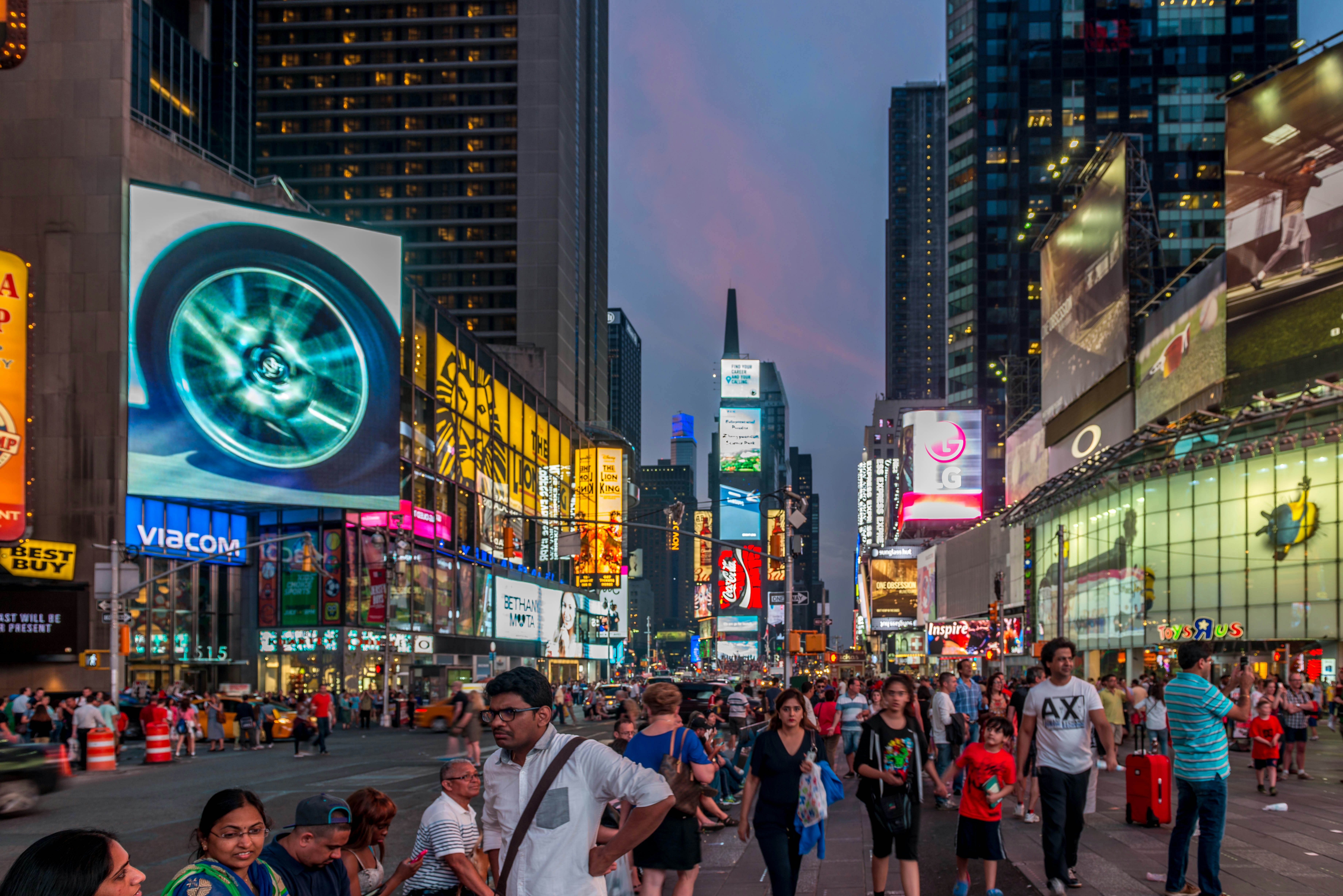 Crowded street scene at dusk with vibrant billboards and illuminated skyscrapers.