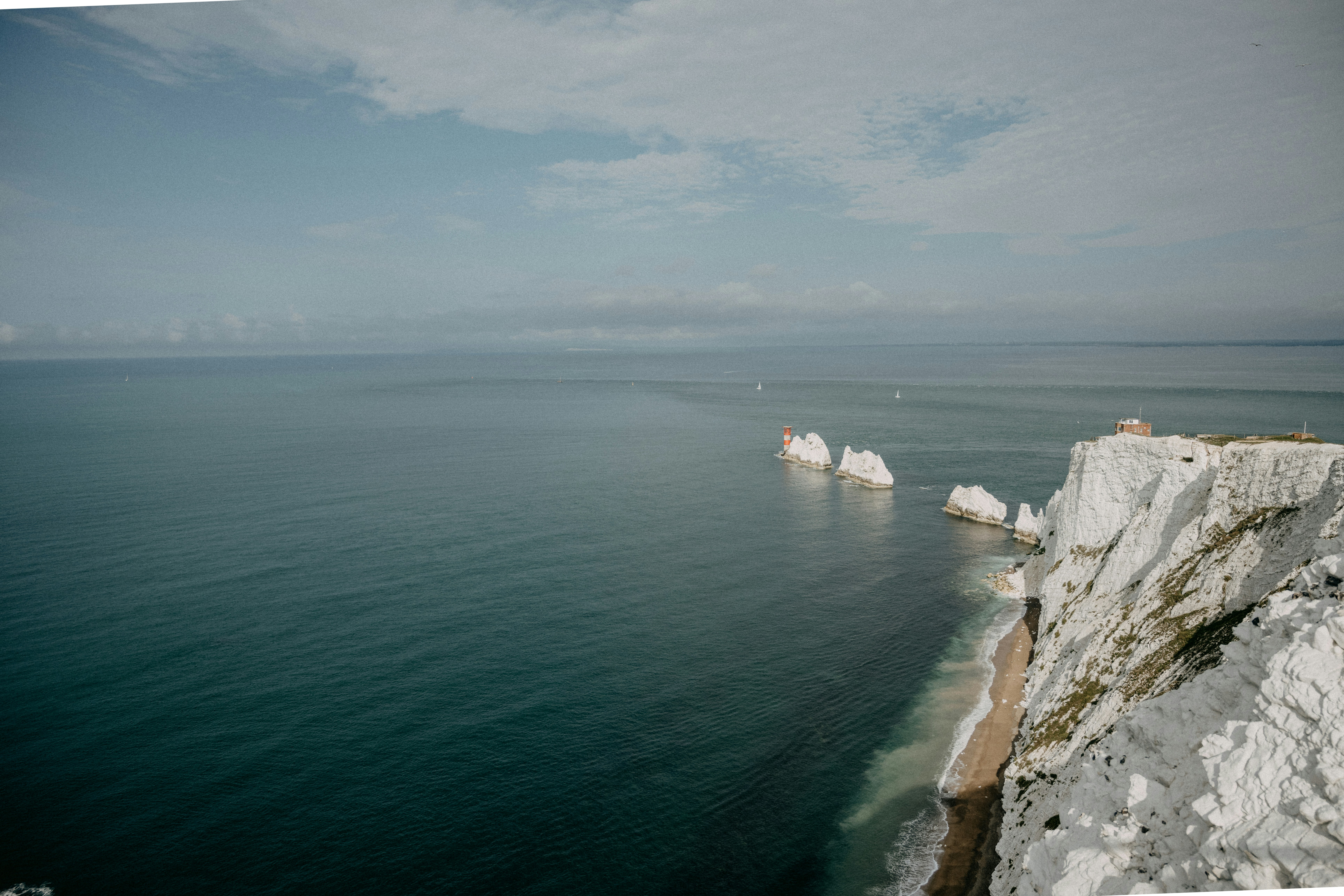 Expansive view of coastal cliffs with scattered rock formations in a calm sea under a cloudy sky.