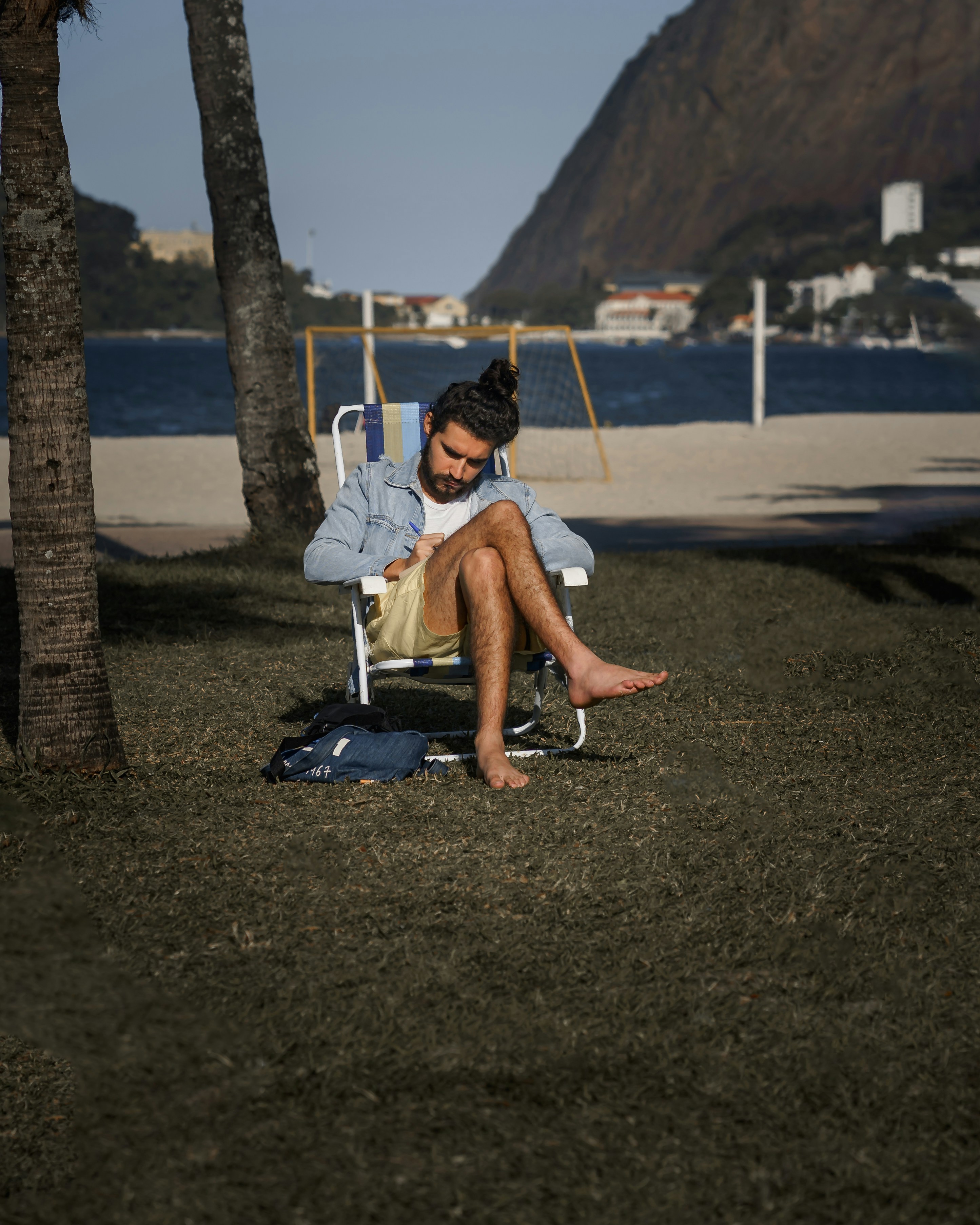 Calm Coastline Moment: A man settles into a beach chair as sea and distant cliffs frame a quiet afternoon