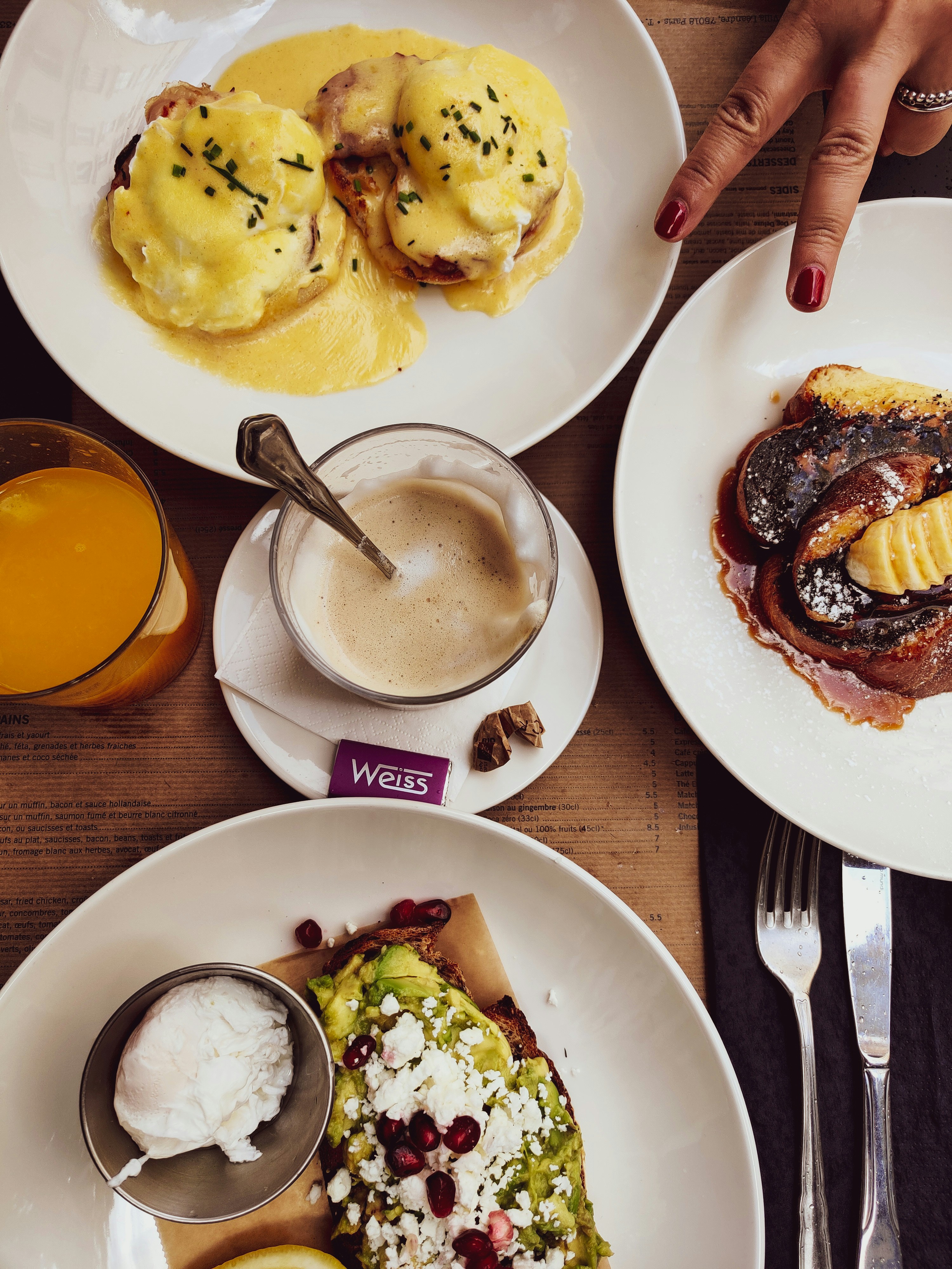 An array of breakfast dishes including eggs Benedict, avocado toast, and pancakes, accompanied by coffee and orange juice, set on a wooden table.