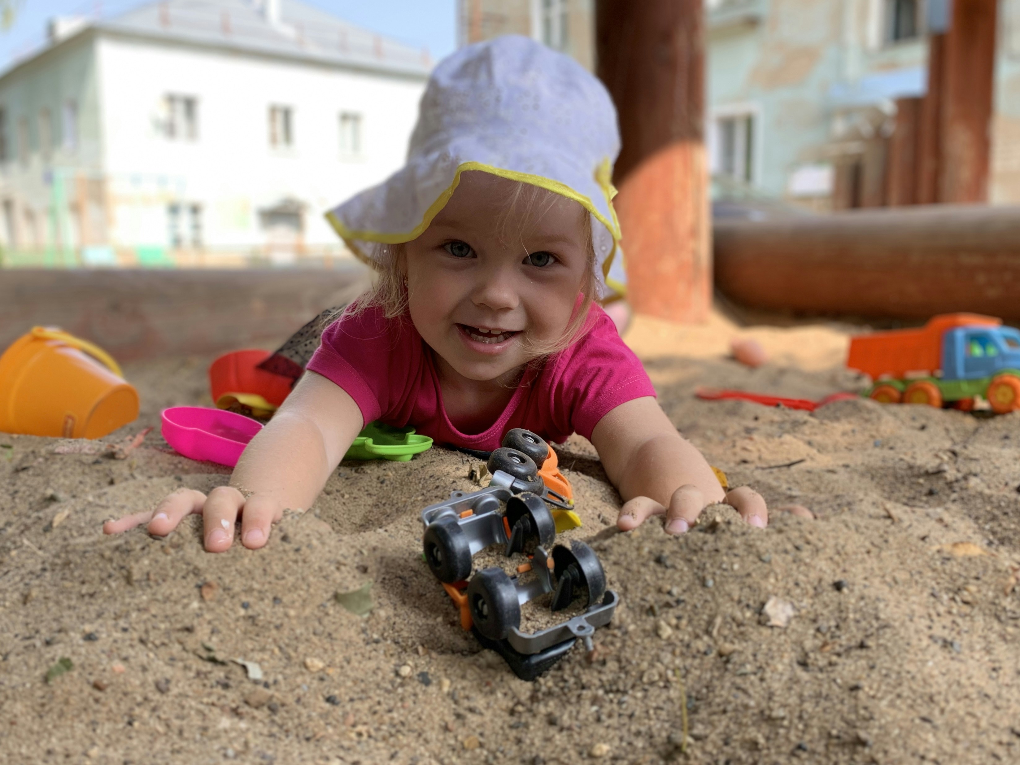 Sandbox Portrait: A toddler's bright grin centers a toy car in sunlit sand