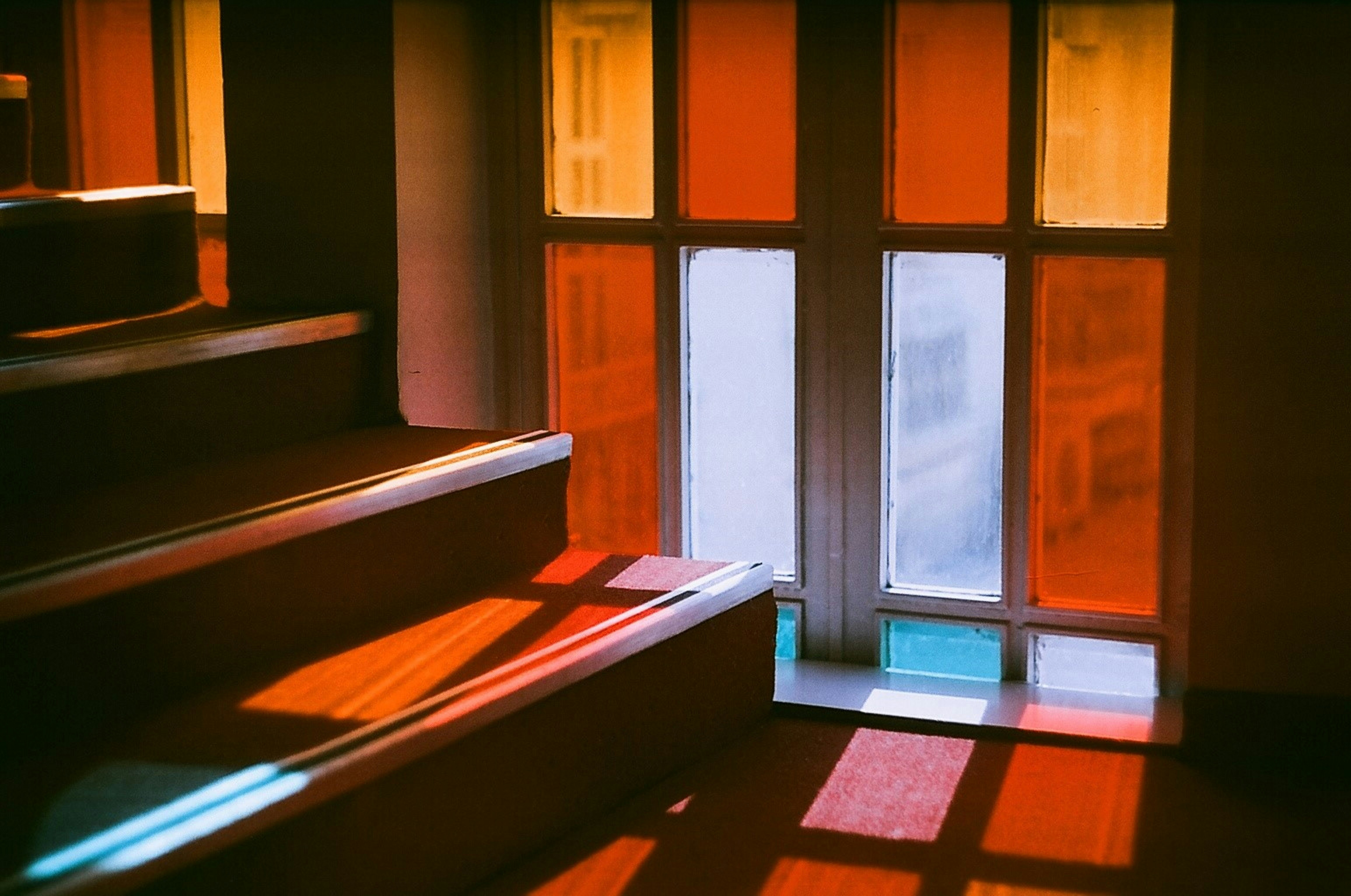 Sunlight casting colorful patterns through stained glass windows onto stairs.