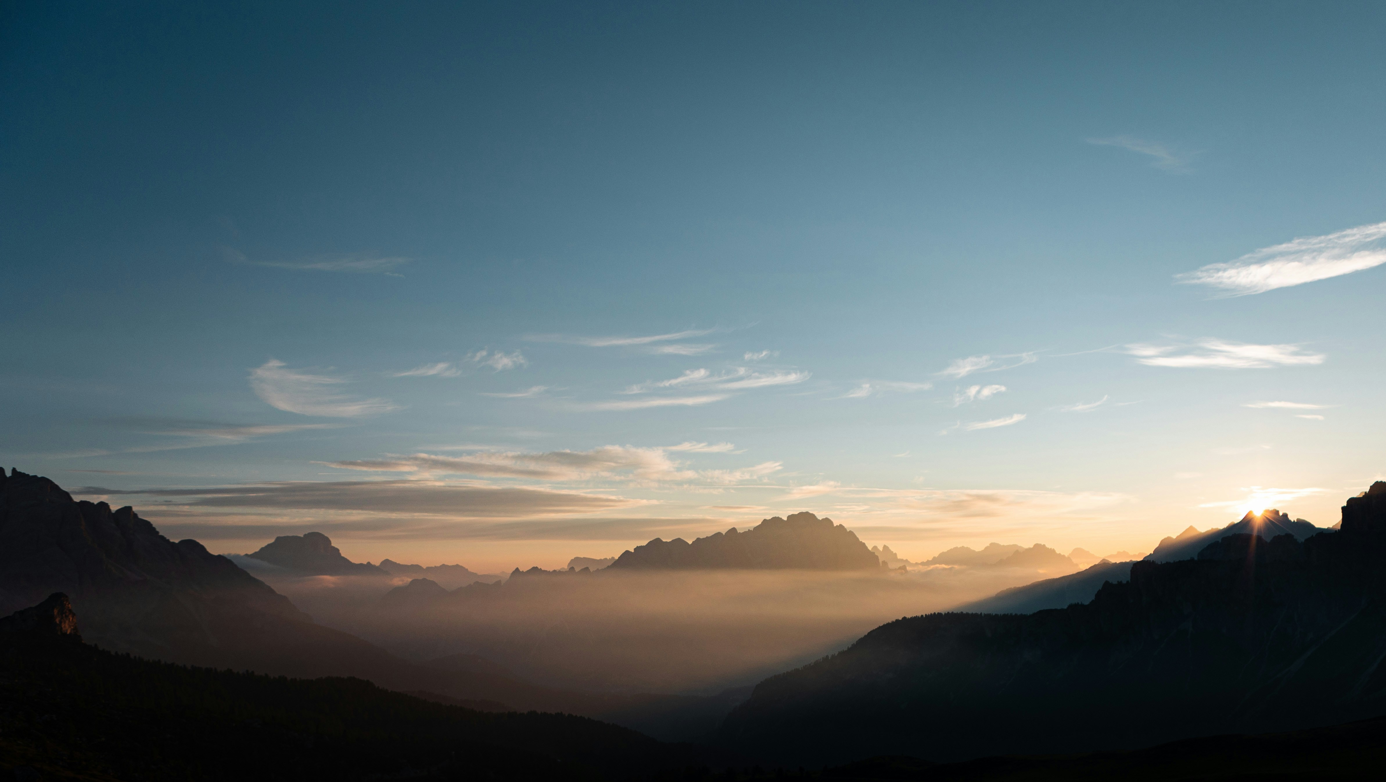 Mountain silhouettes under a pastel sky at sunrise, with mist filling the valleys.