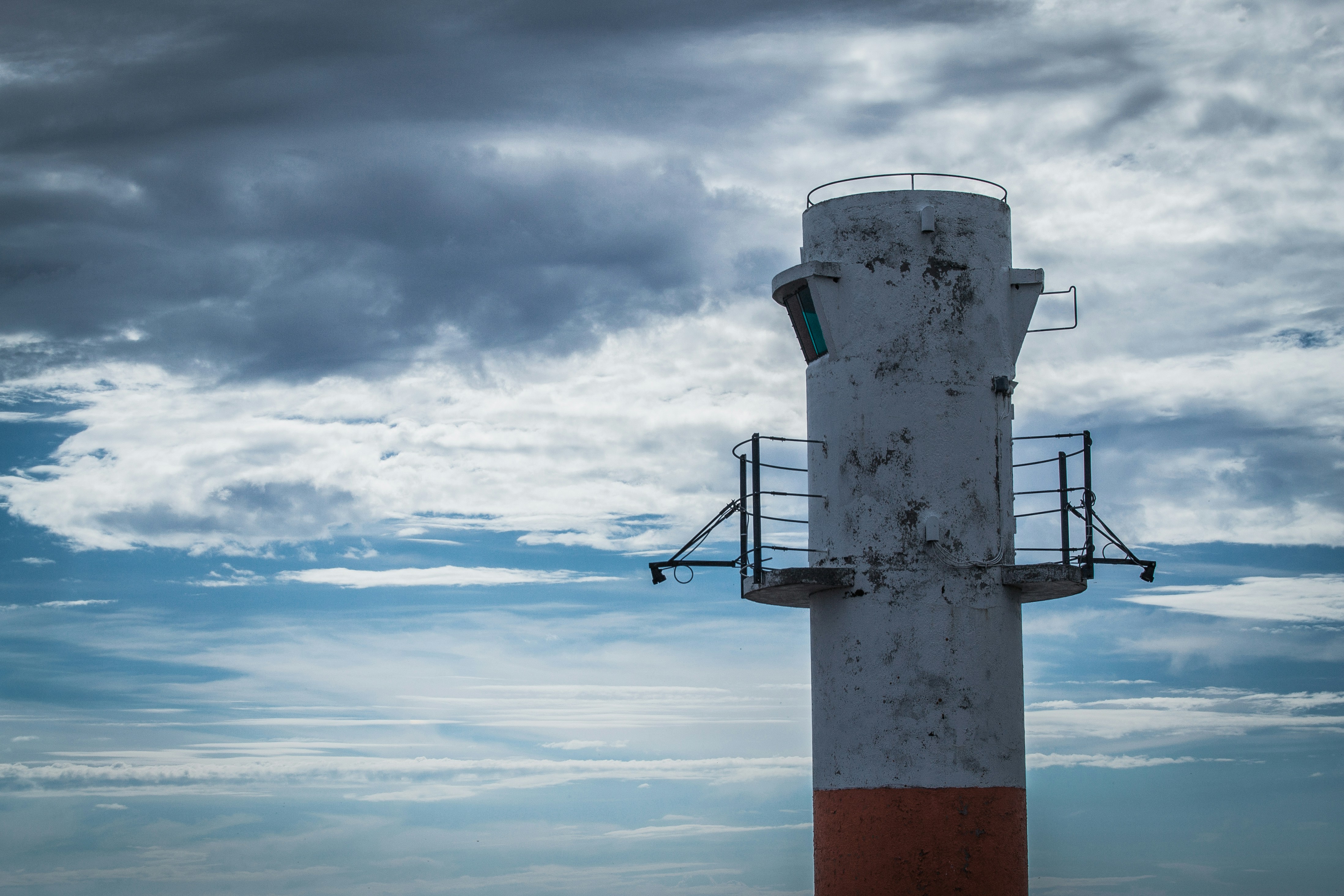A weathered lighthouse rises against a dramatic sky, showcasing its sturdy structure and the interplay of light and clouds.