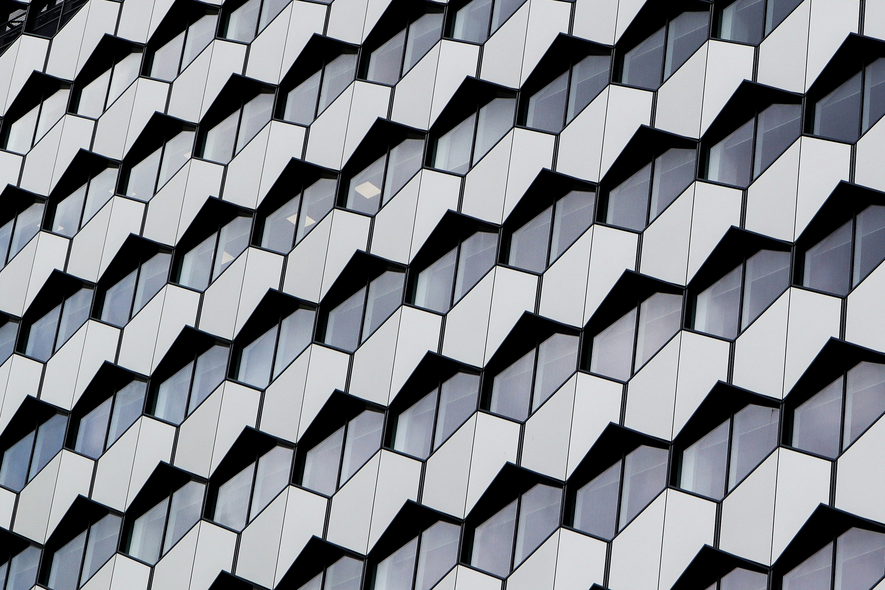 Close-up of a modern building facade featuring a unique hexagonal pattern of windows and panels. The interplay of light and shadow highlights the architectural design.