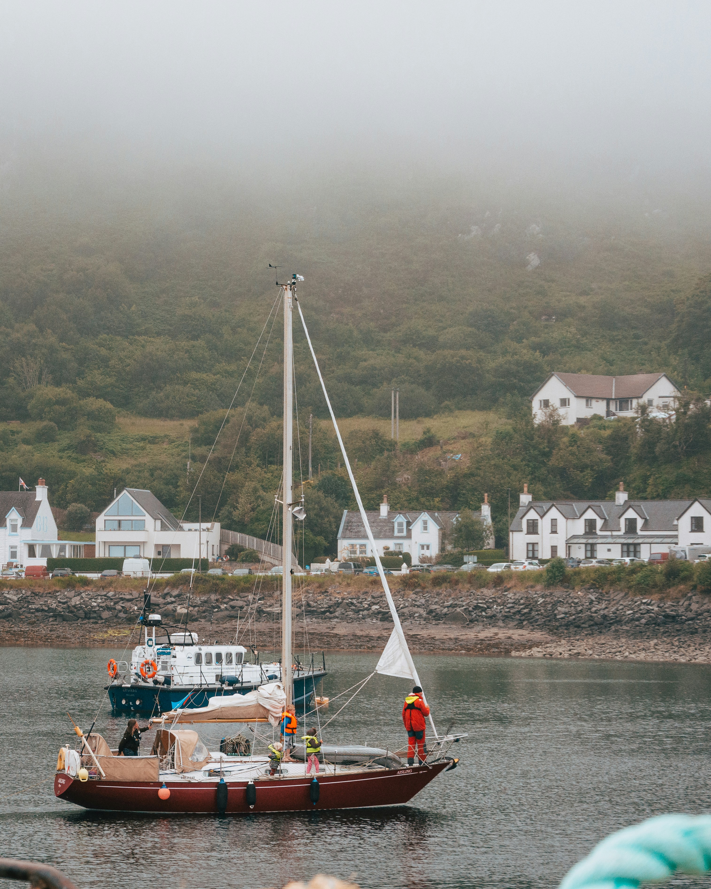 Crimson-hulled Sailboat in Morning Fog Above a Quiet Coastal Village